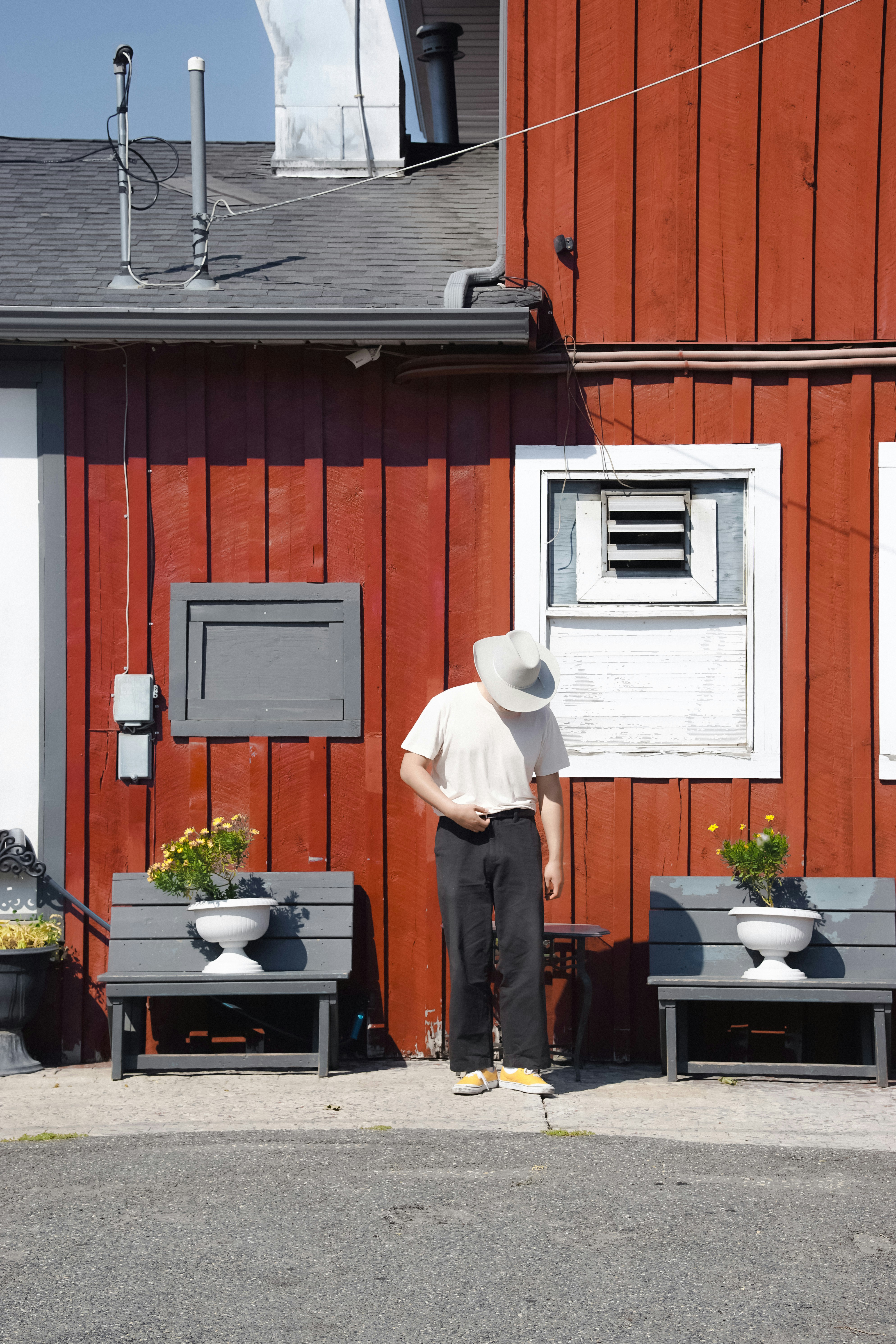 White-Hatted Quiet: A solitary figure framed by a red clapboard facade