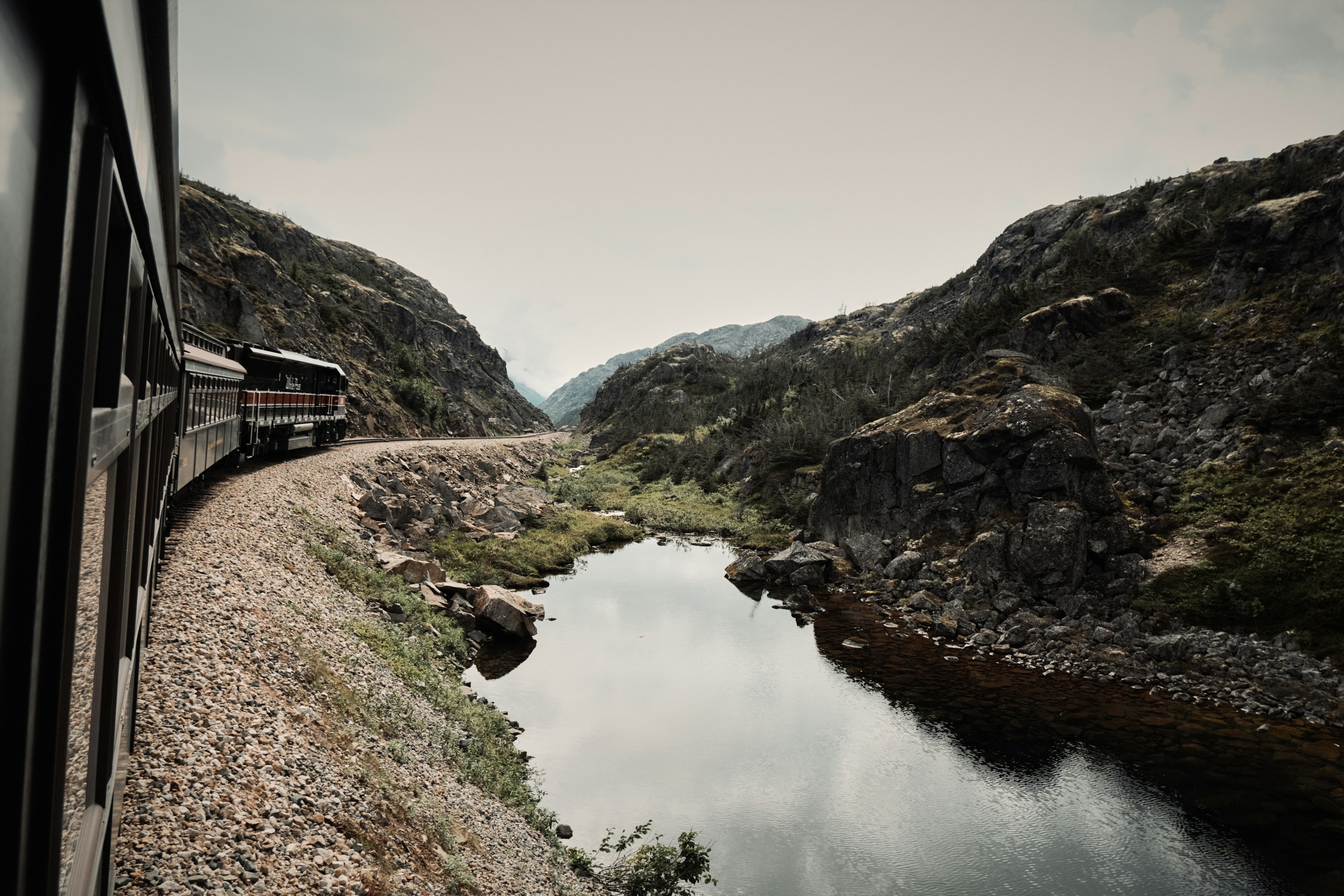 A train traveling down tracks next to a body of water photo – Free ...