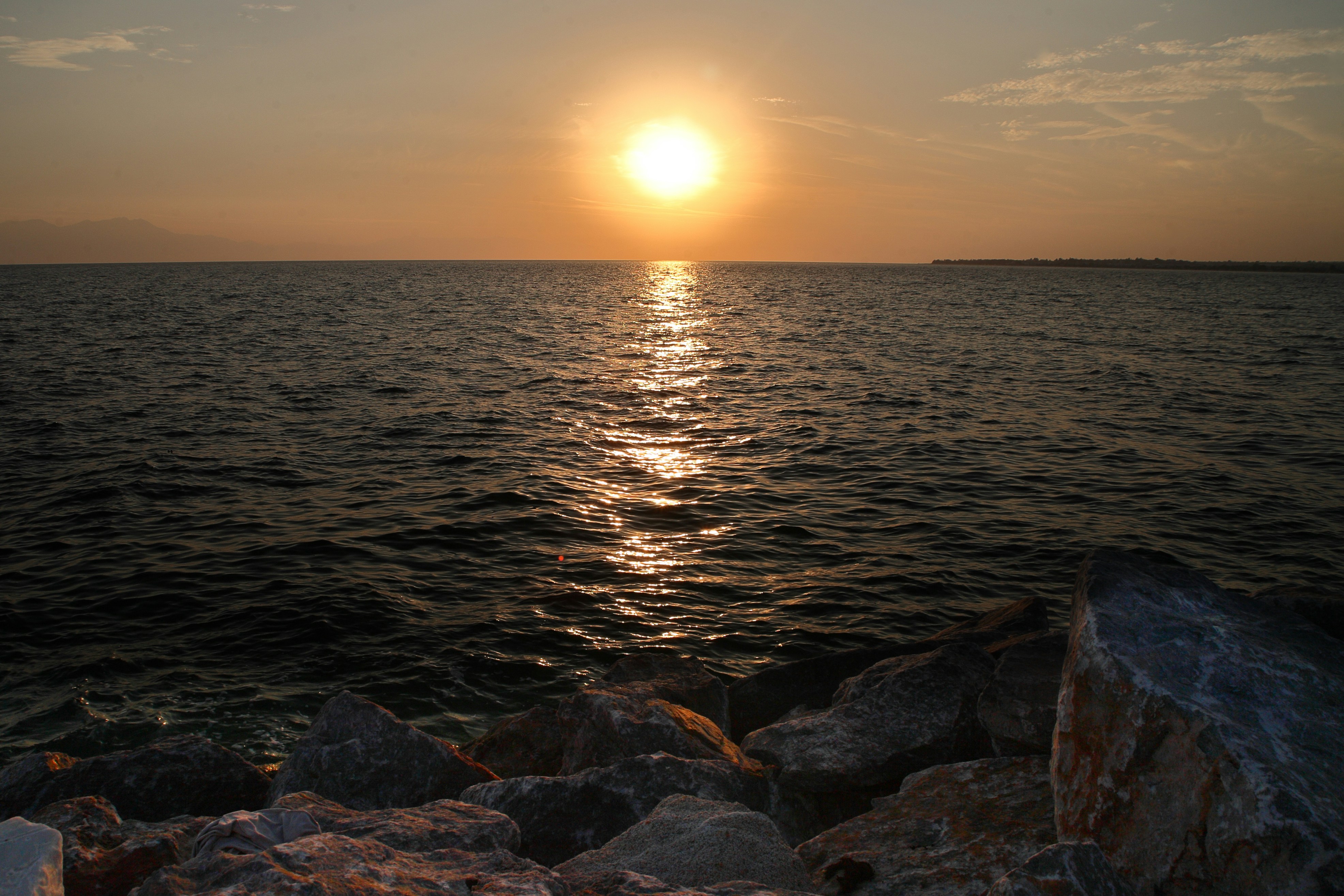 Sunset casting warm hues over a calm sea with rocky foreground.