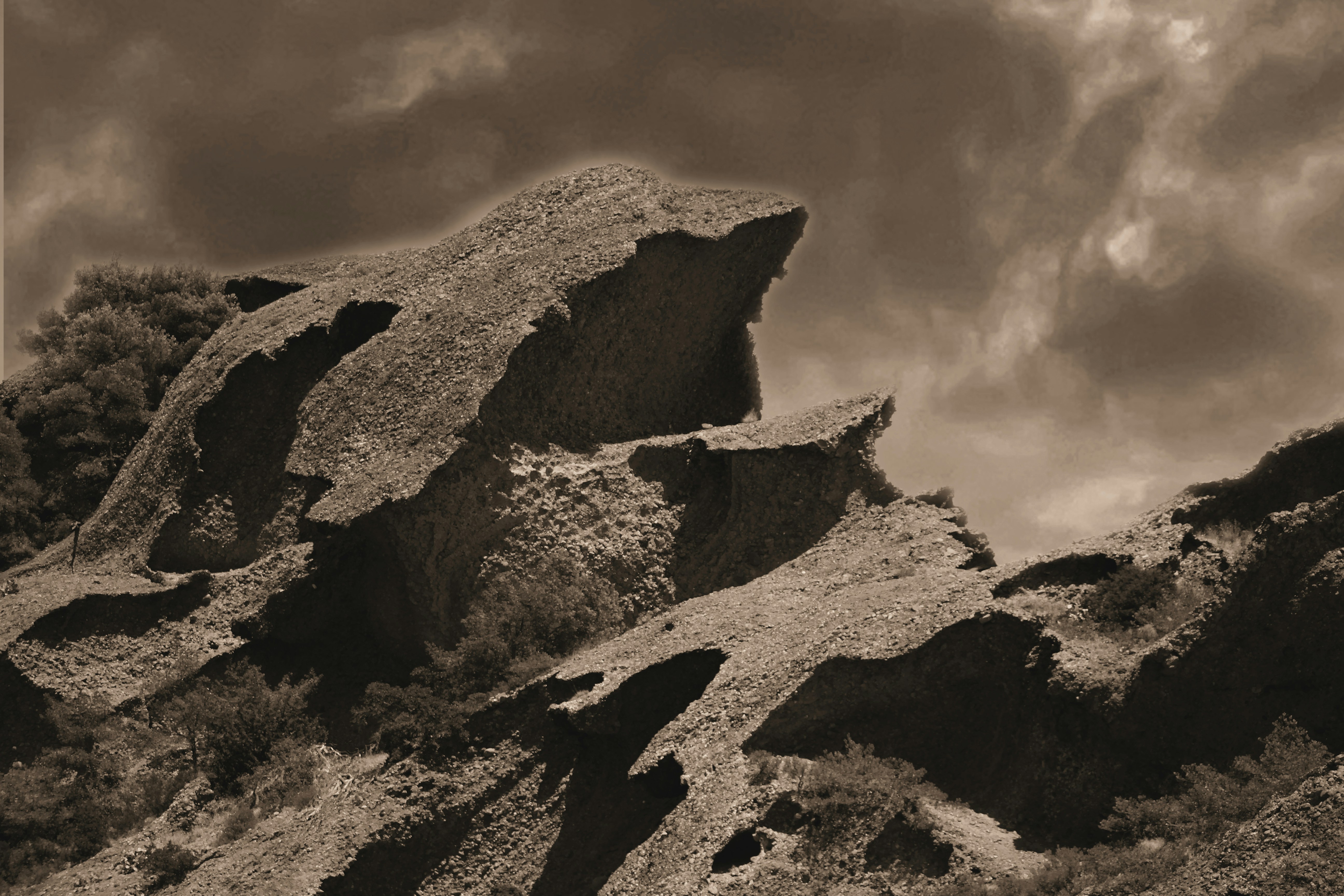 Jagged rock formations rise dramatically against a moody sky, showcasing the power of natural erosion. The monochromatic tones enhance the rugged texture of the landscape.