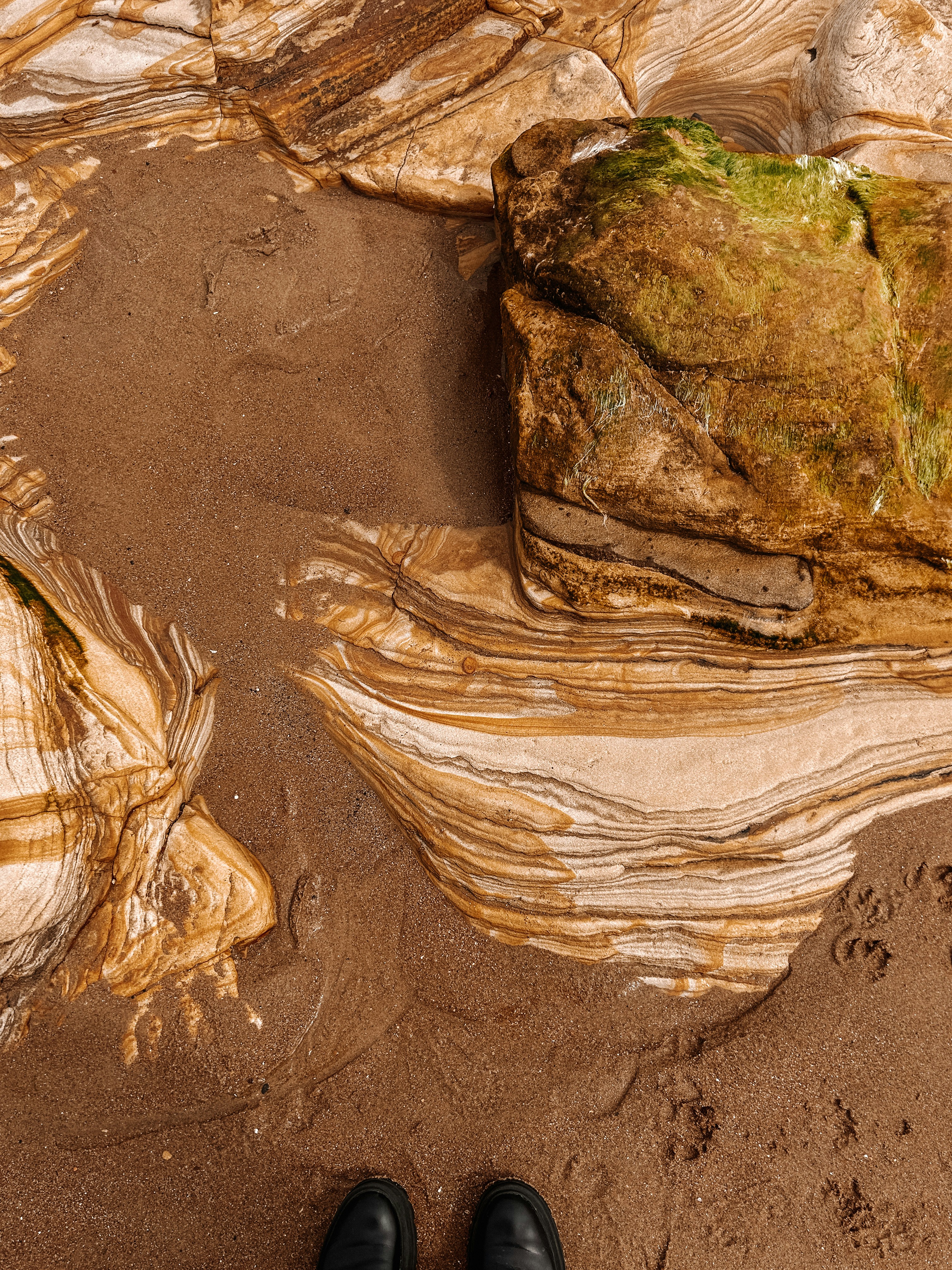 Layered tide-worn rocks meet sandy shoreline underfoot