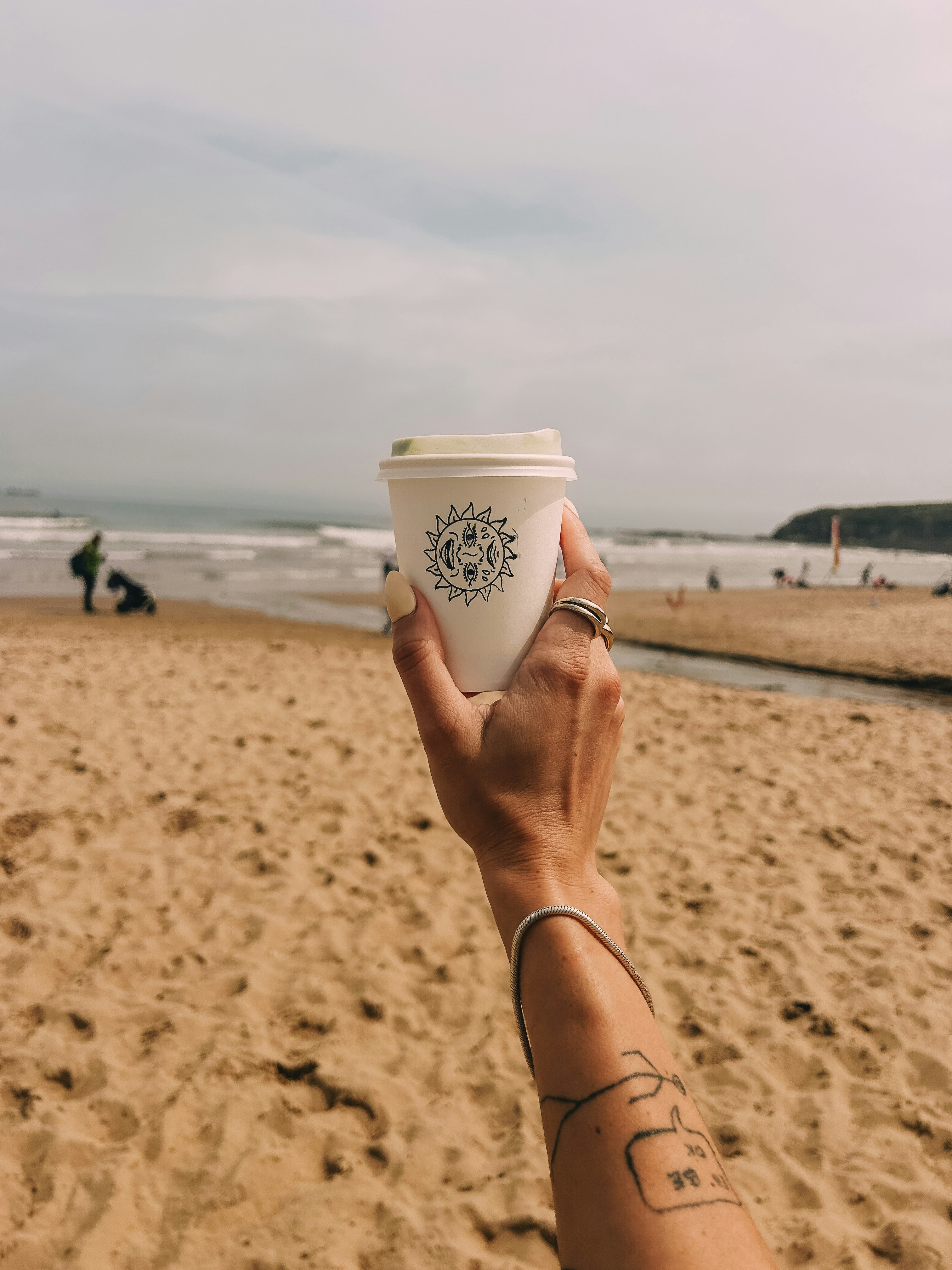 A person holding up a cup of coffee on a beach
