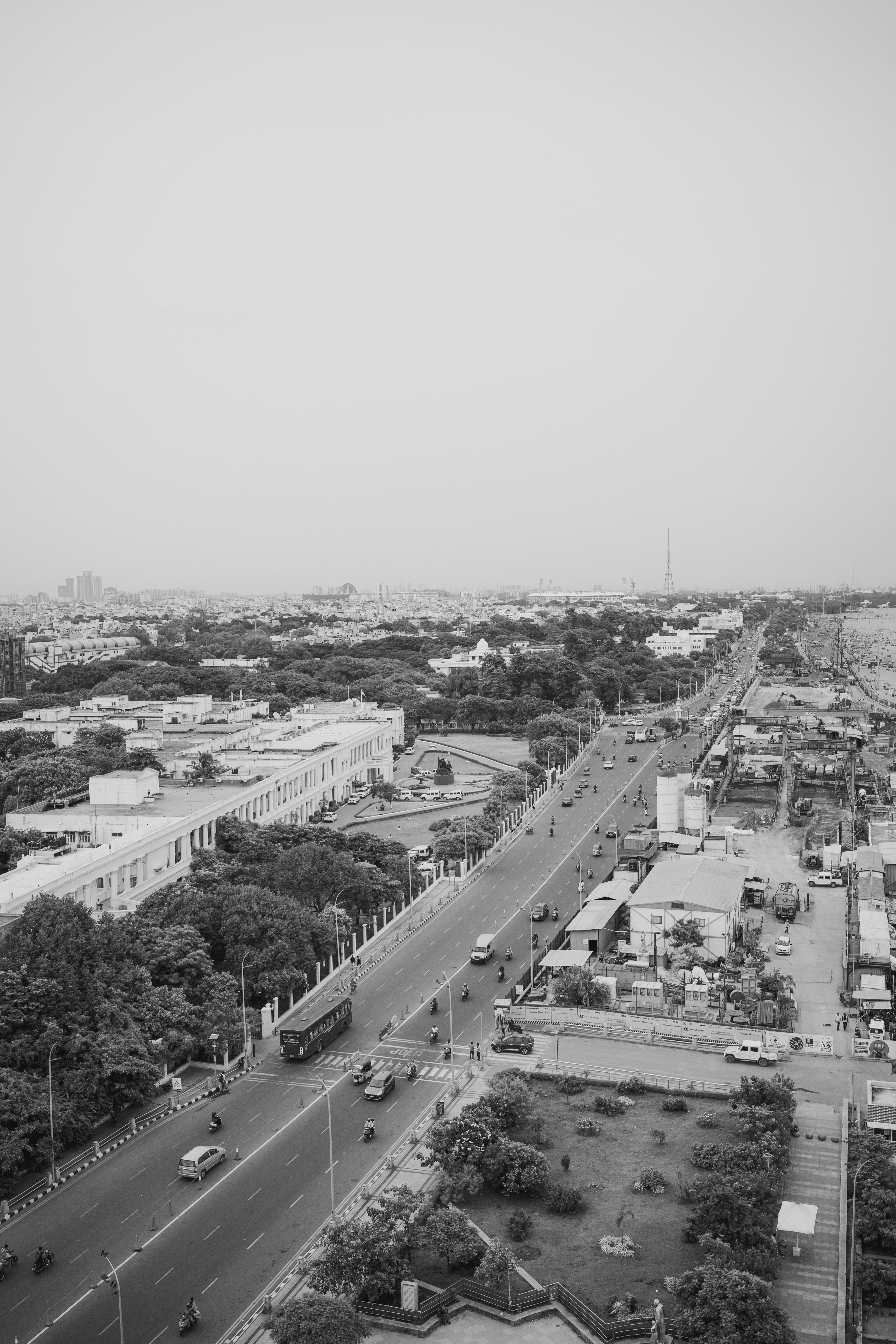 Aerial view of a bustling cityscape, showcasing roads, vehicles, and greenery in a monochromatic palette. The image highlights the dynamic interplay between urban development and nature.