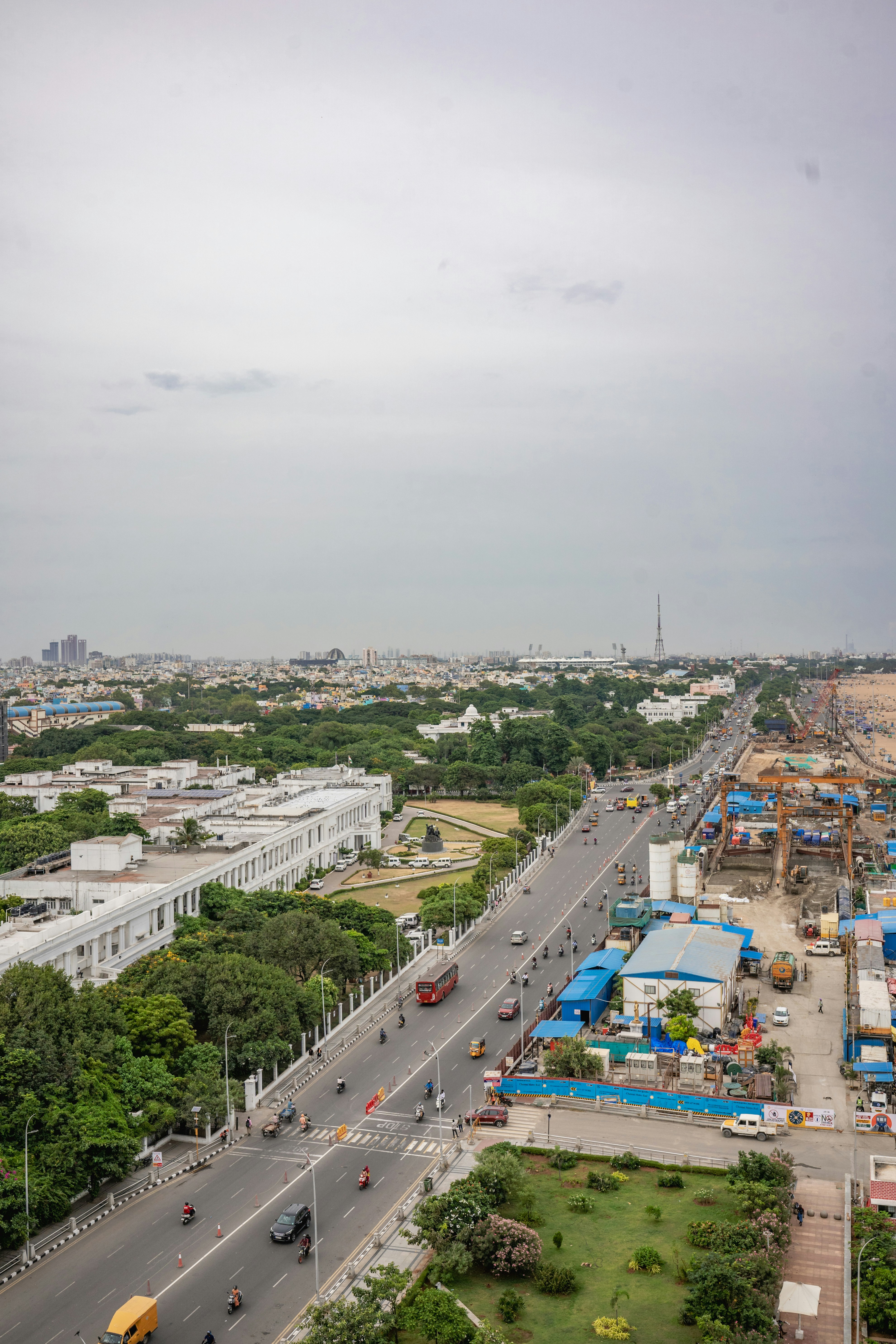 Aerial view of a bustling cityscape featuring a blend of greenery, urban infrastructure, and ongoing construction activities. The scene captures the dynamic nature of urban development.