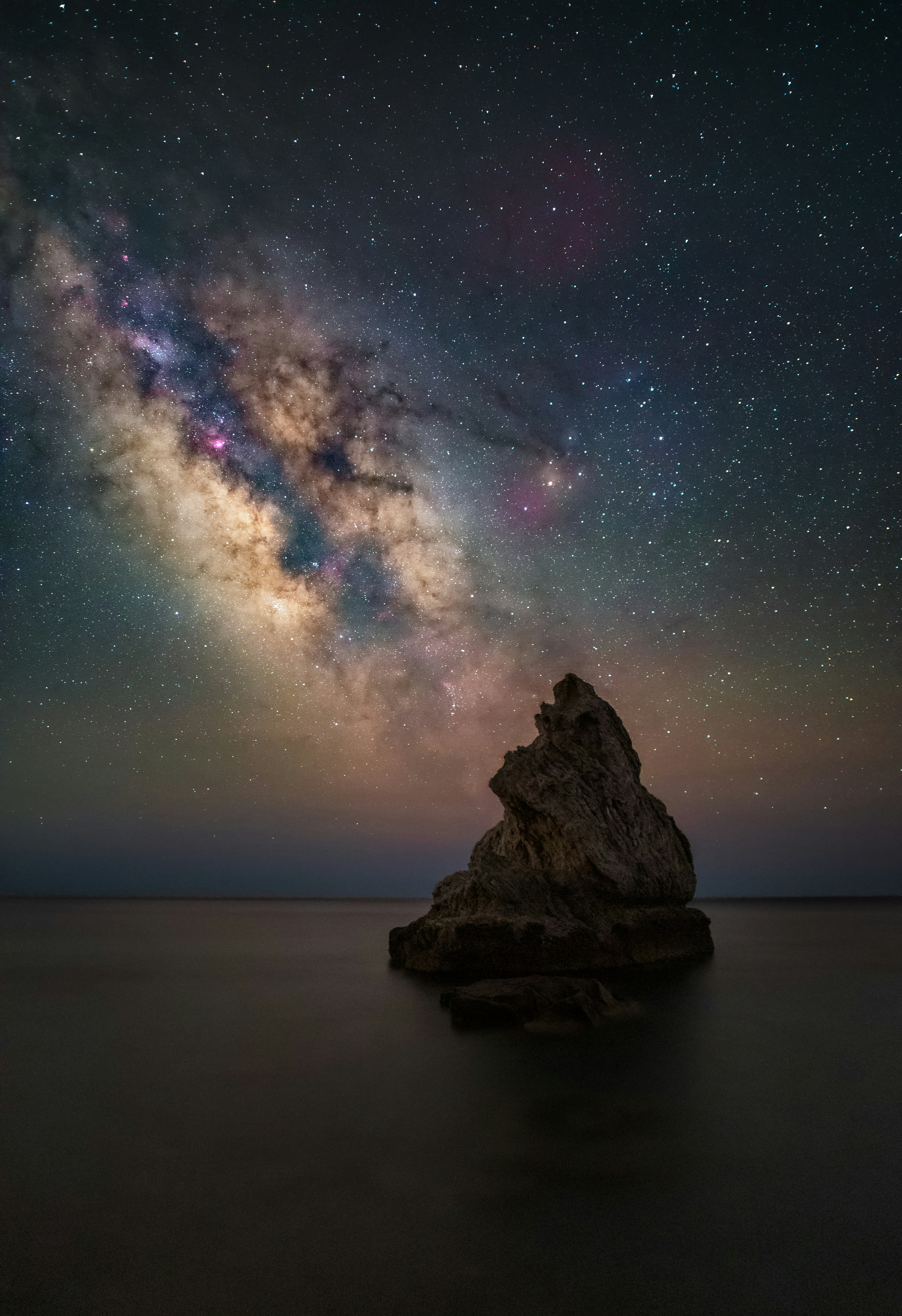 A rock in the middle of a body of water under a night sky filled with