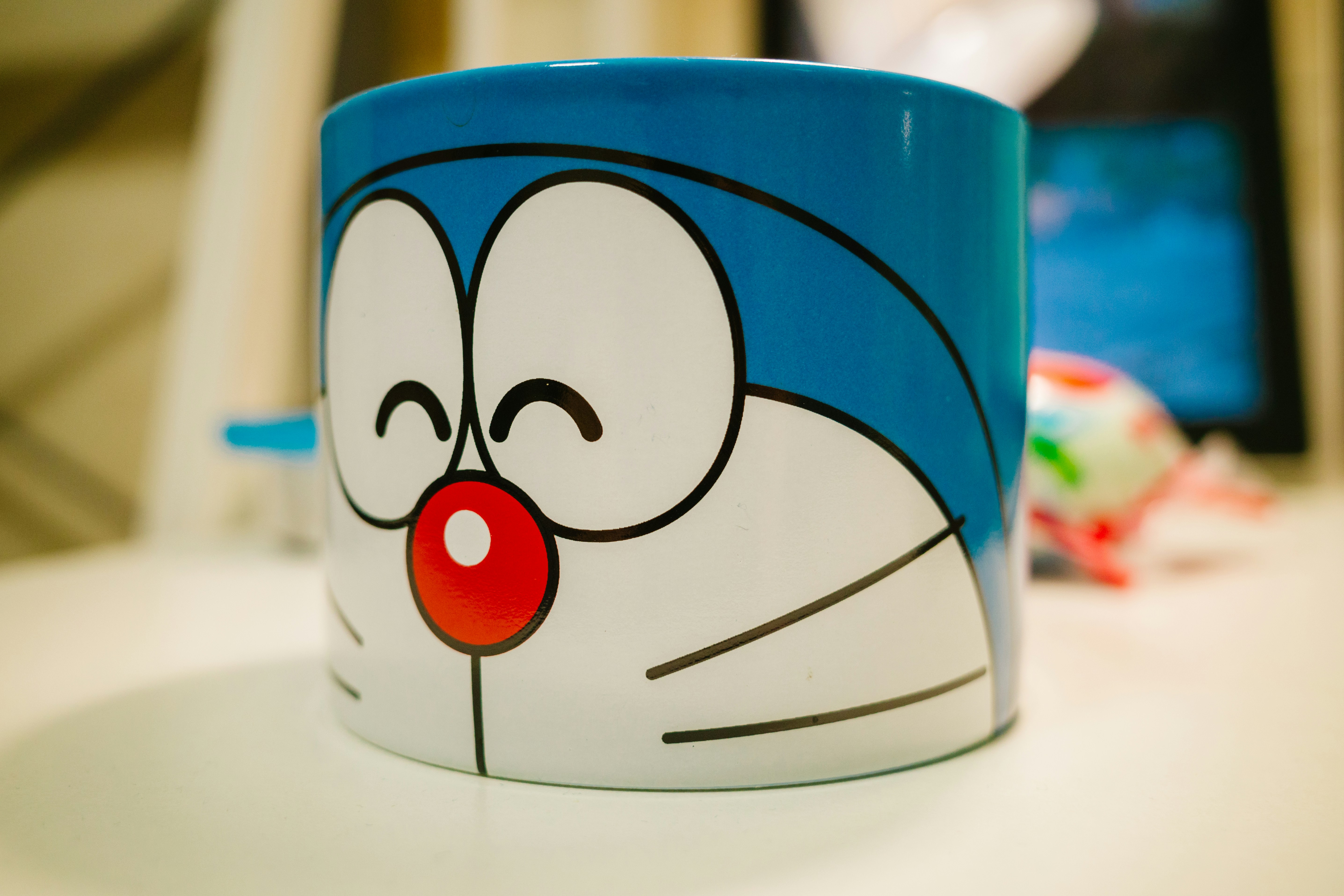 Doraemon on a White Desk: Close-Up of a Blue Ceramic Mug with Cartoon Charm