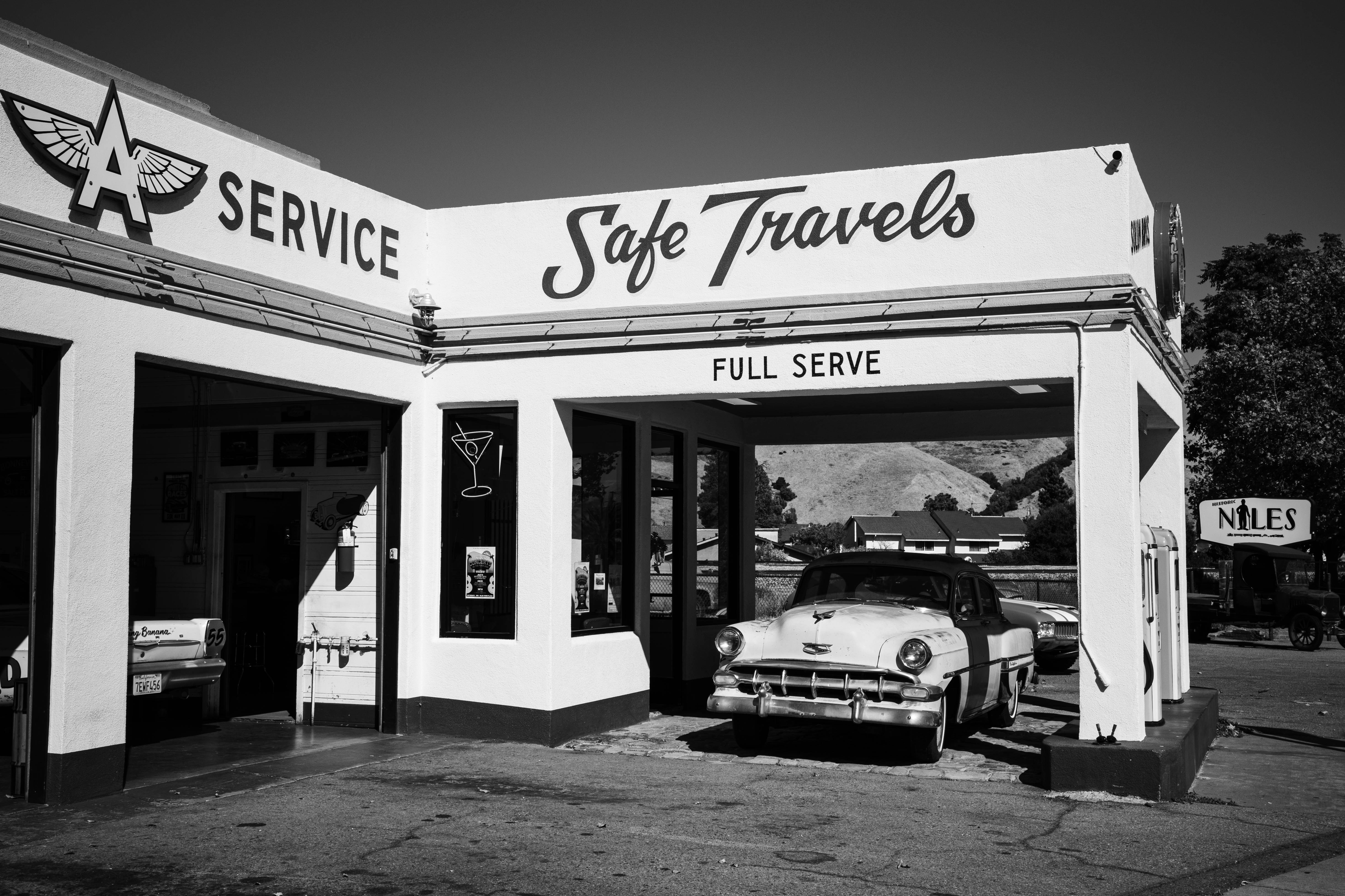 Under the Safe Travels canopy: a mid-century car rests at a retro service station