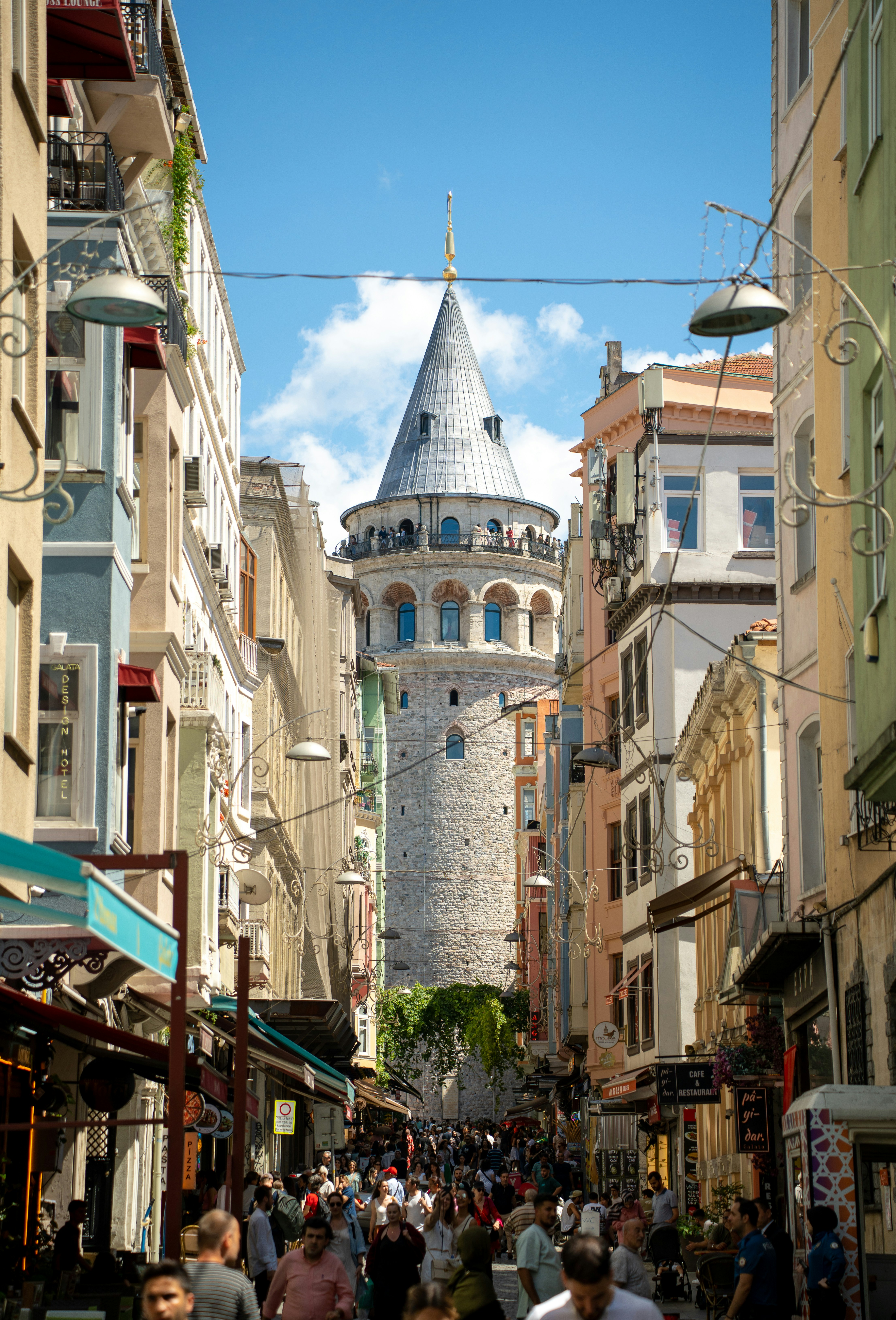 Galata Tower in Focus: A Sunlit Corridor of Colorful Facades and Crowds