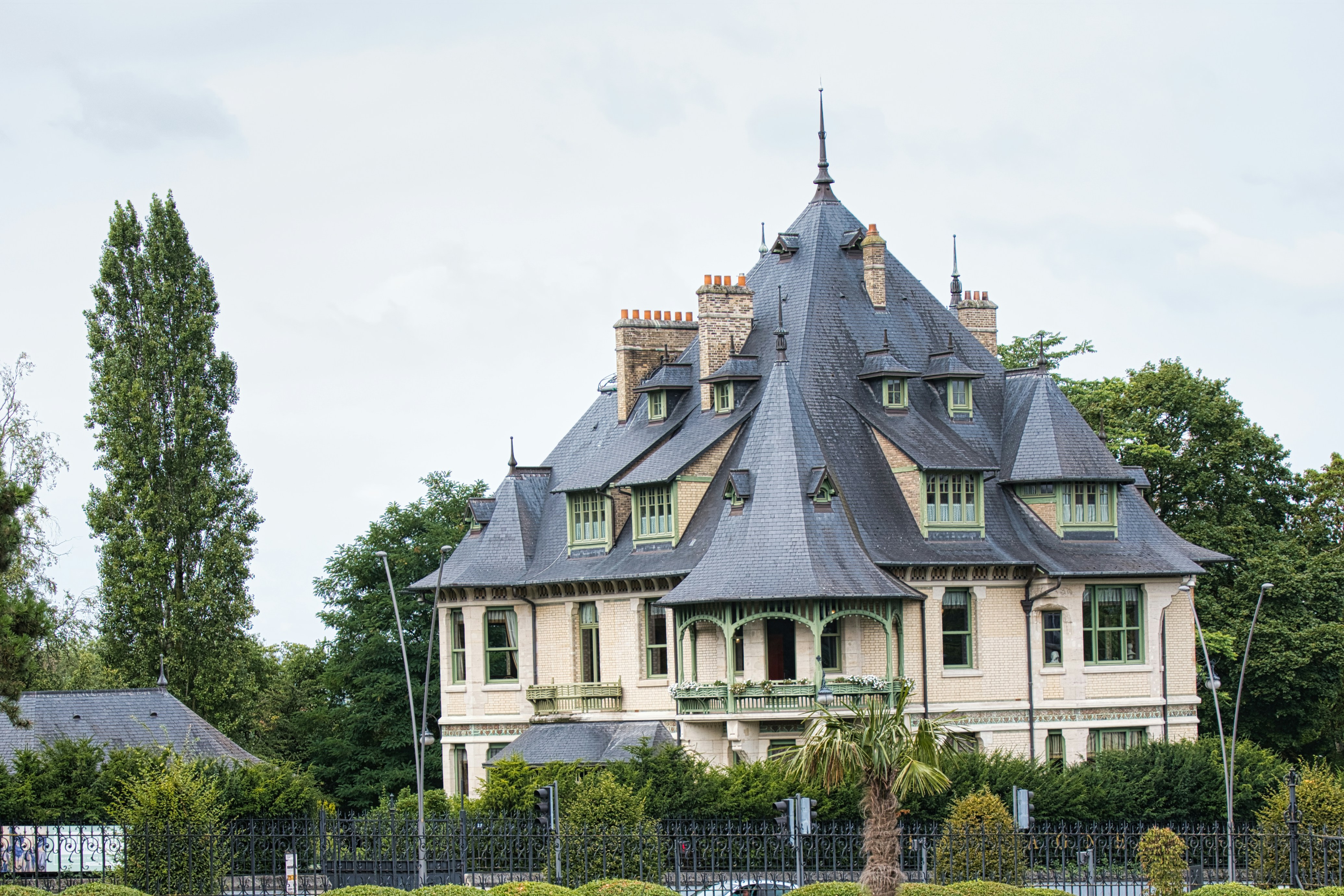 Large Victorian-style house with a steep black roof and ornate details surrounded by lush greenery.