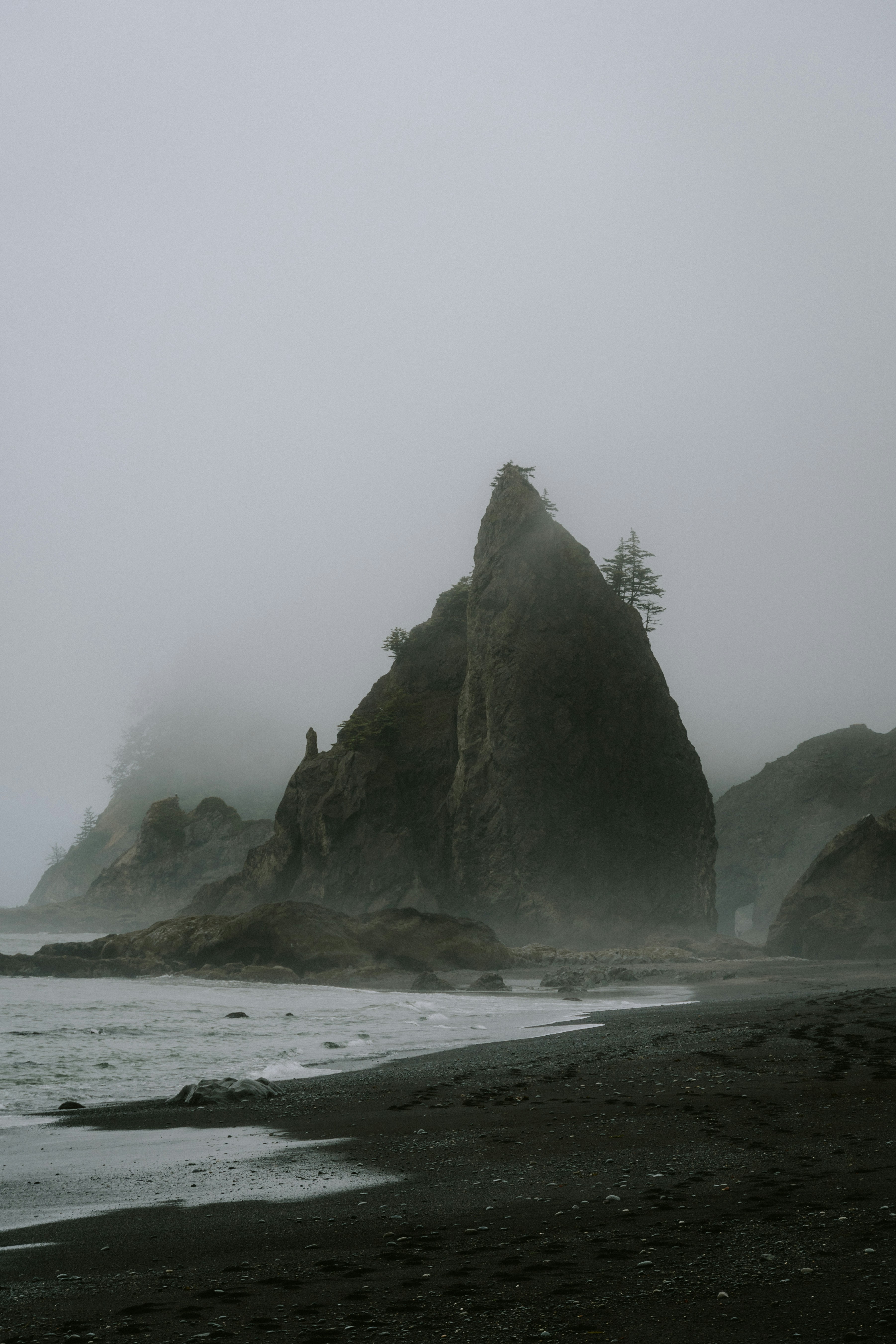 A foggy beach with a large rock formation in the foreground photo ...