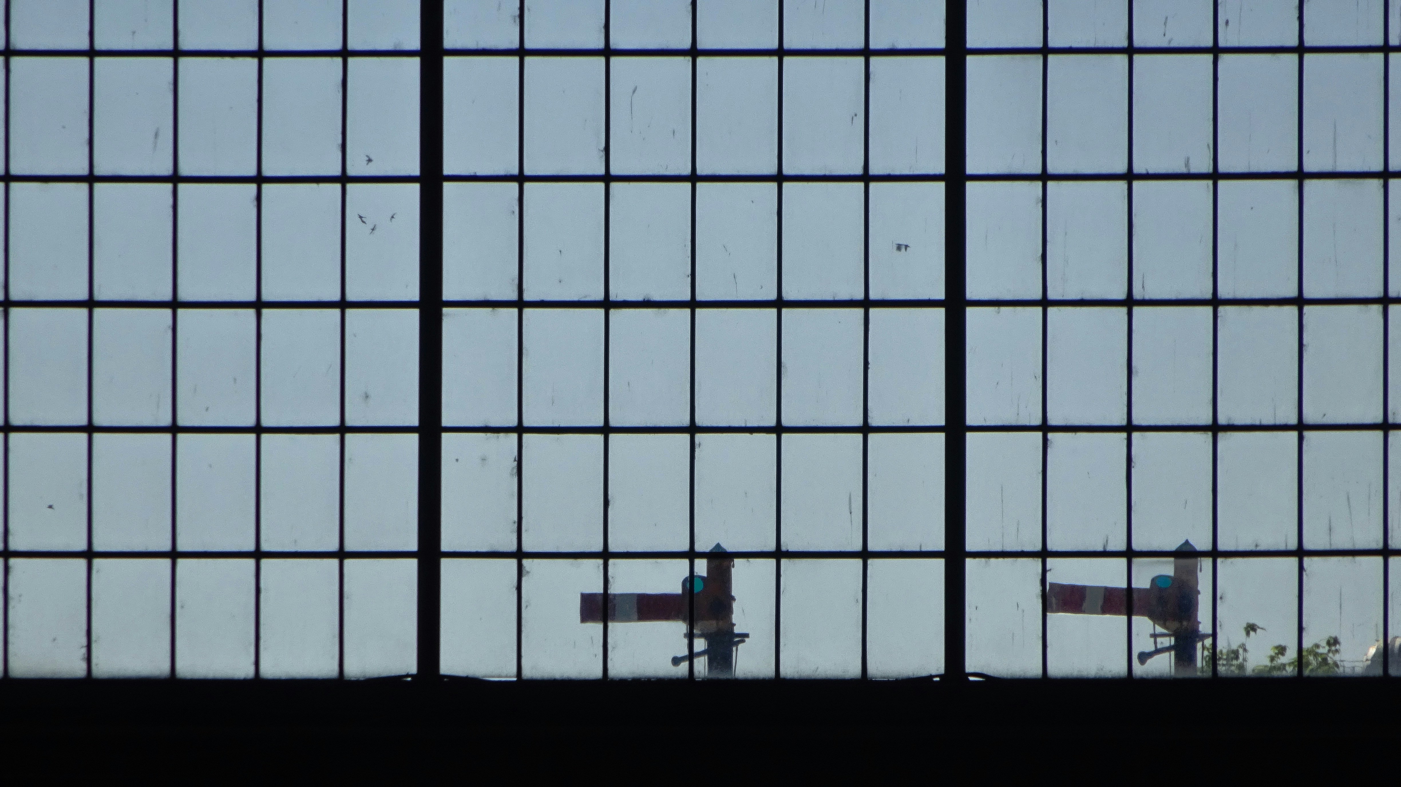 Two tiny model airplanes appear behind a weathered grid against a pale blue sky.
