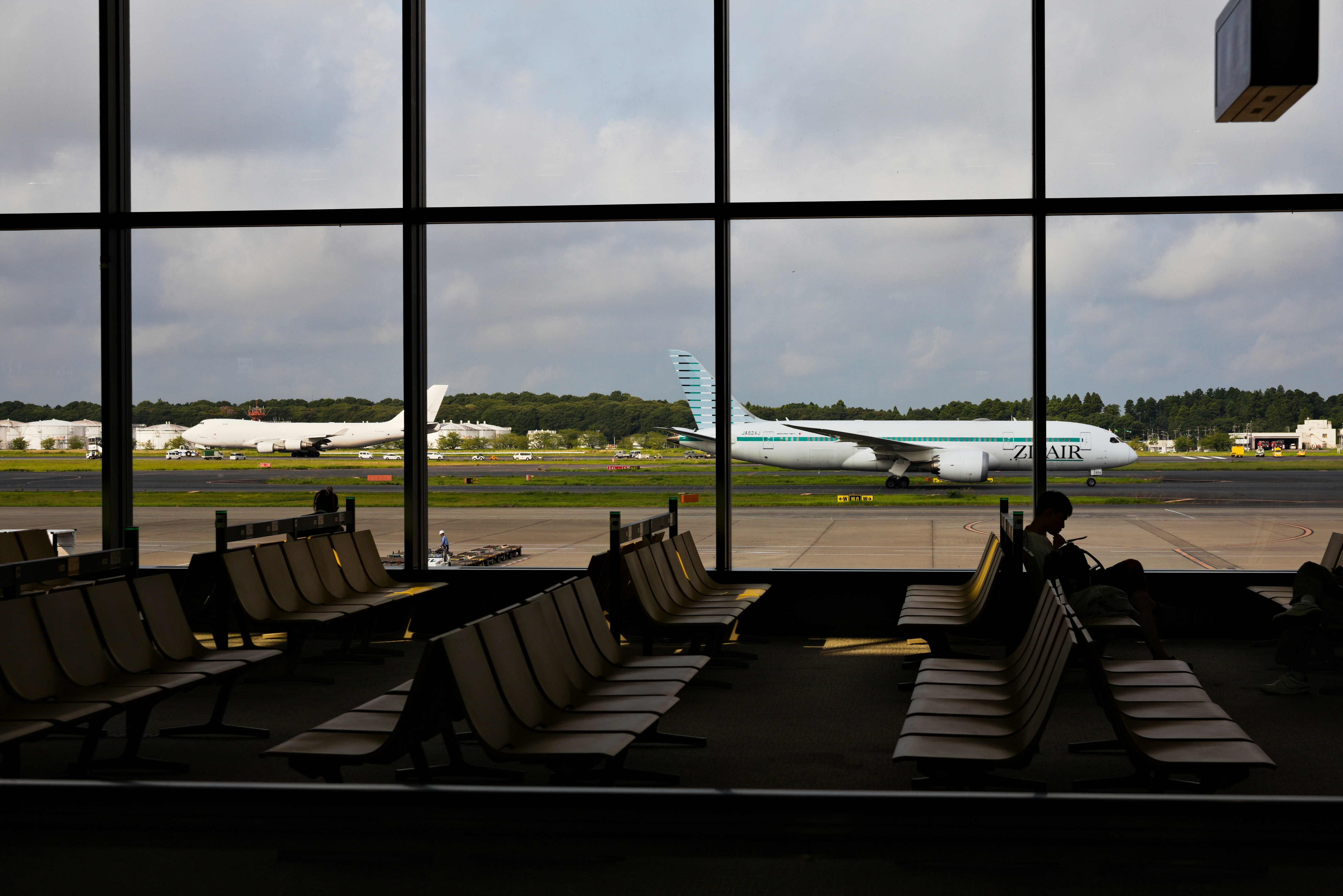 Empty airport seating with a plane visible through large windows under a cloudy sky.
