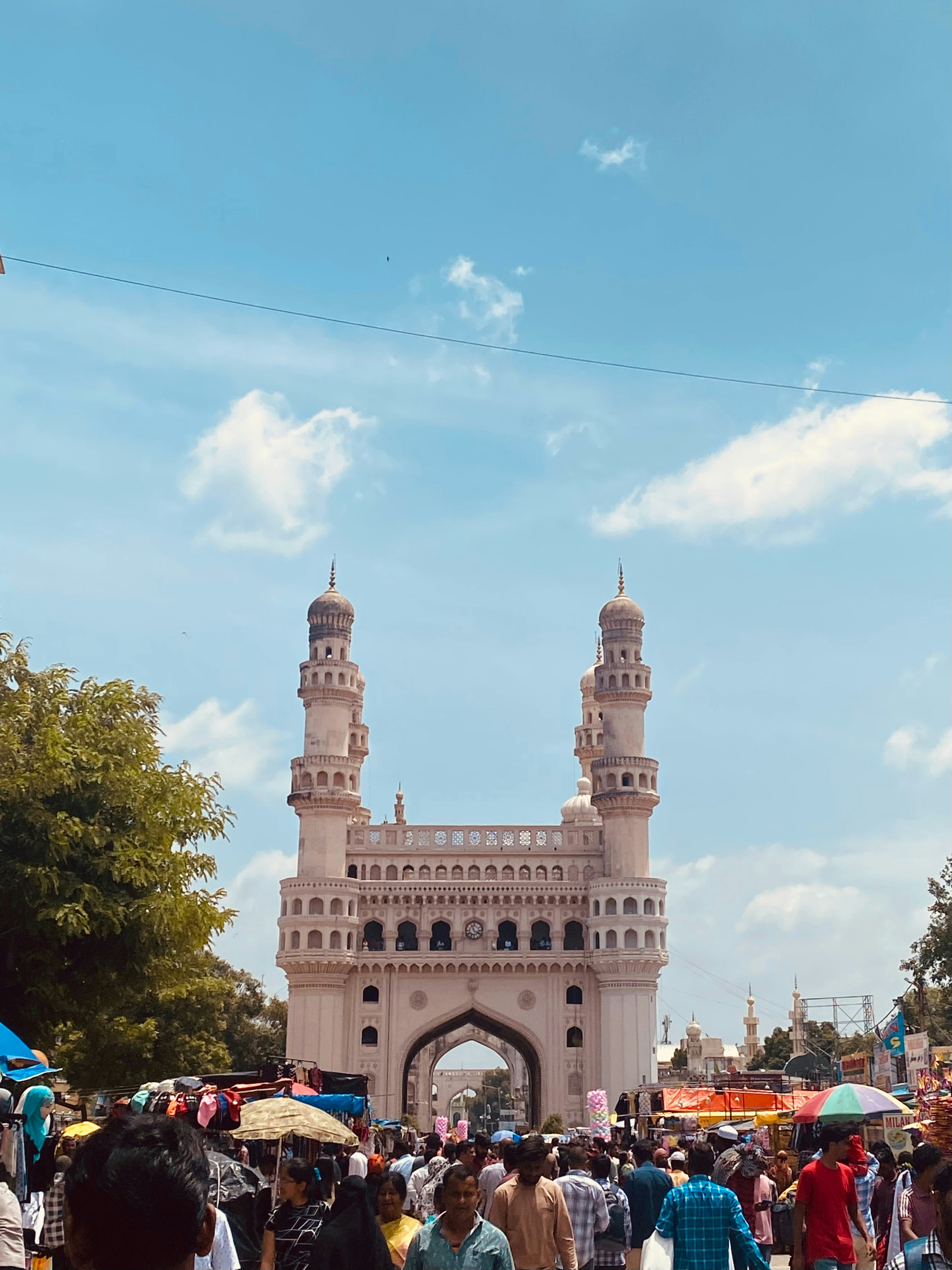 Iconic monument framed by bustling market scene, showcasing the lively atmosphere of the area. Bright blue sky complements the architectural details.