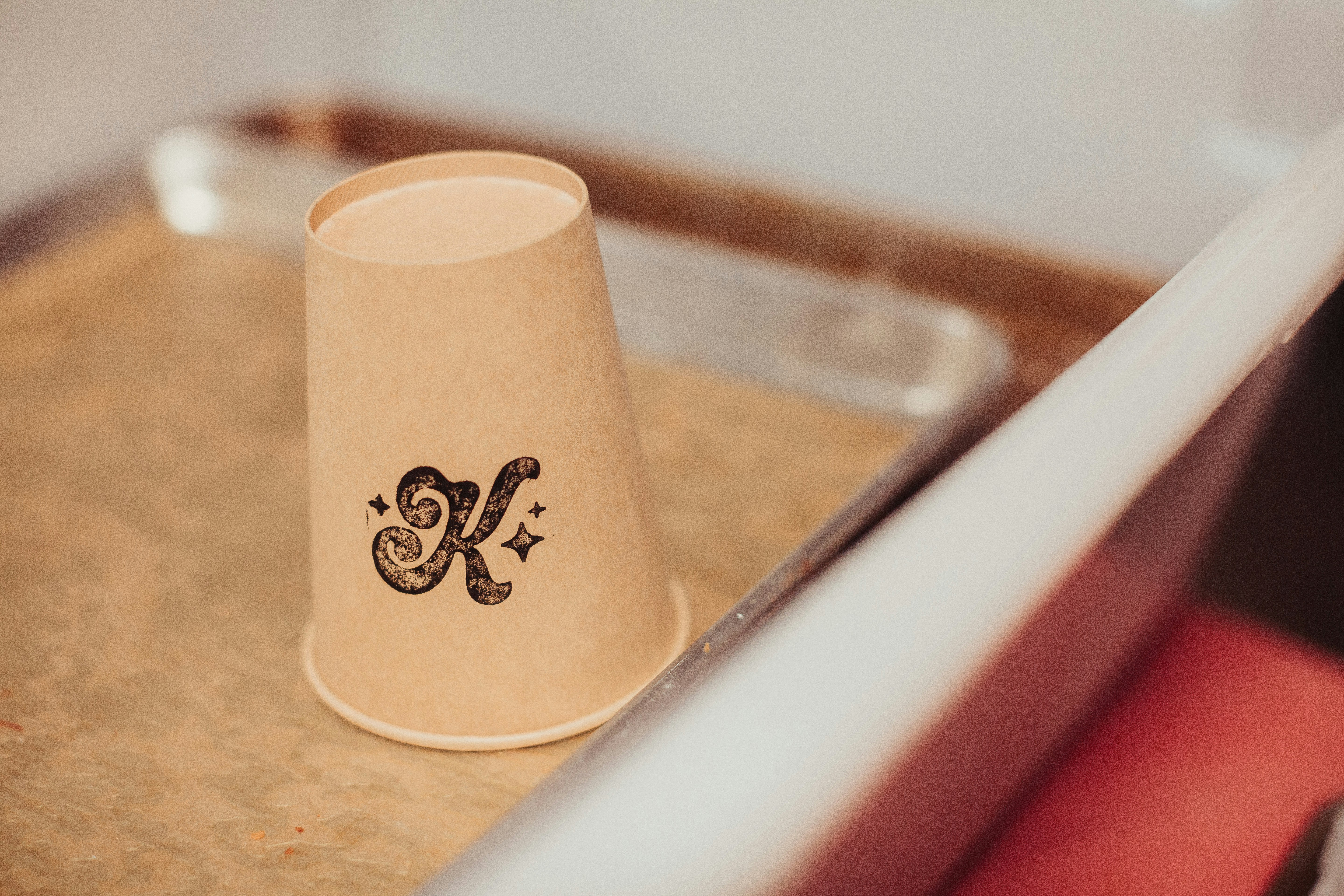 A lone paper cup with engraved K rests beside a kitchen sink edge