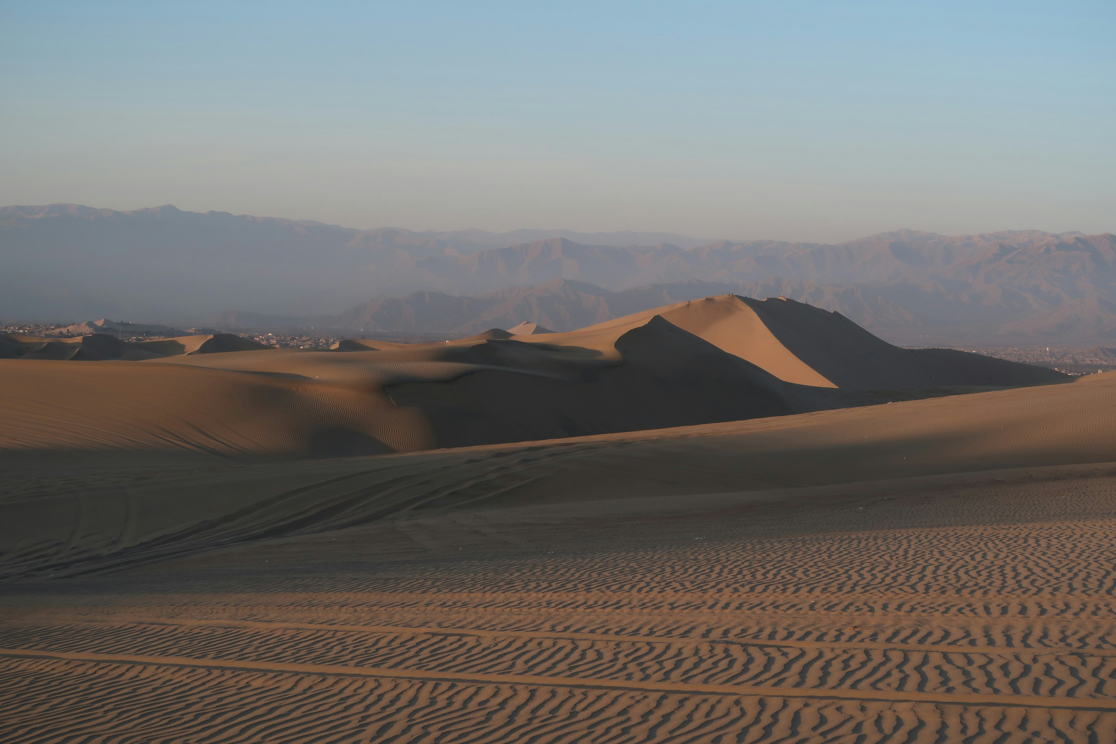 Golden sand dunes with soft shadows under a clear blue sky in the Ica desert.