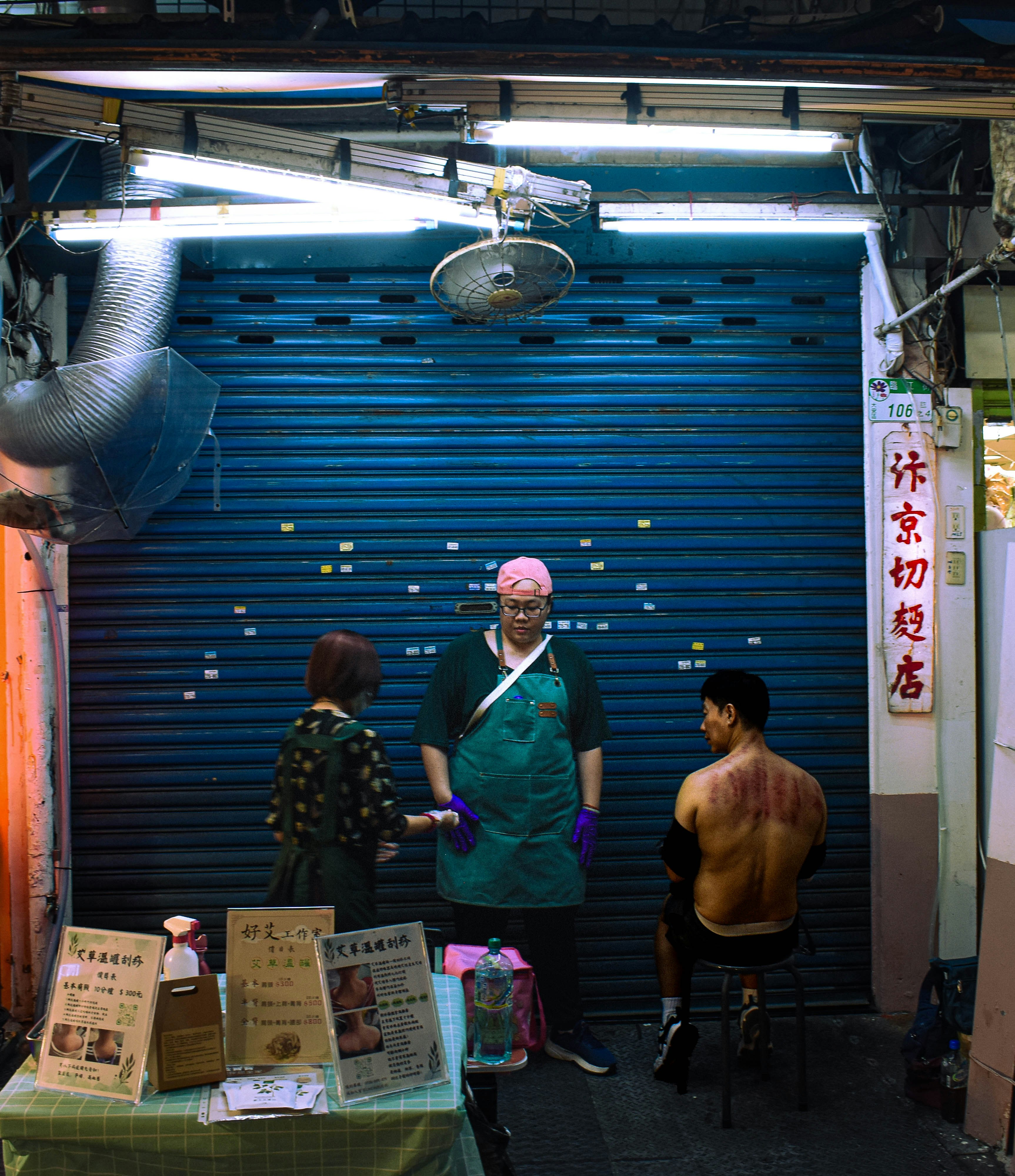 Blue Shutter Night: Teal Apron Vendor under Neon Fluorescence