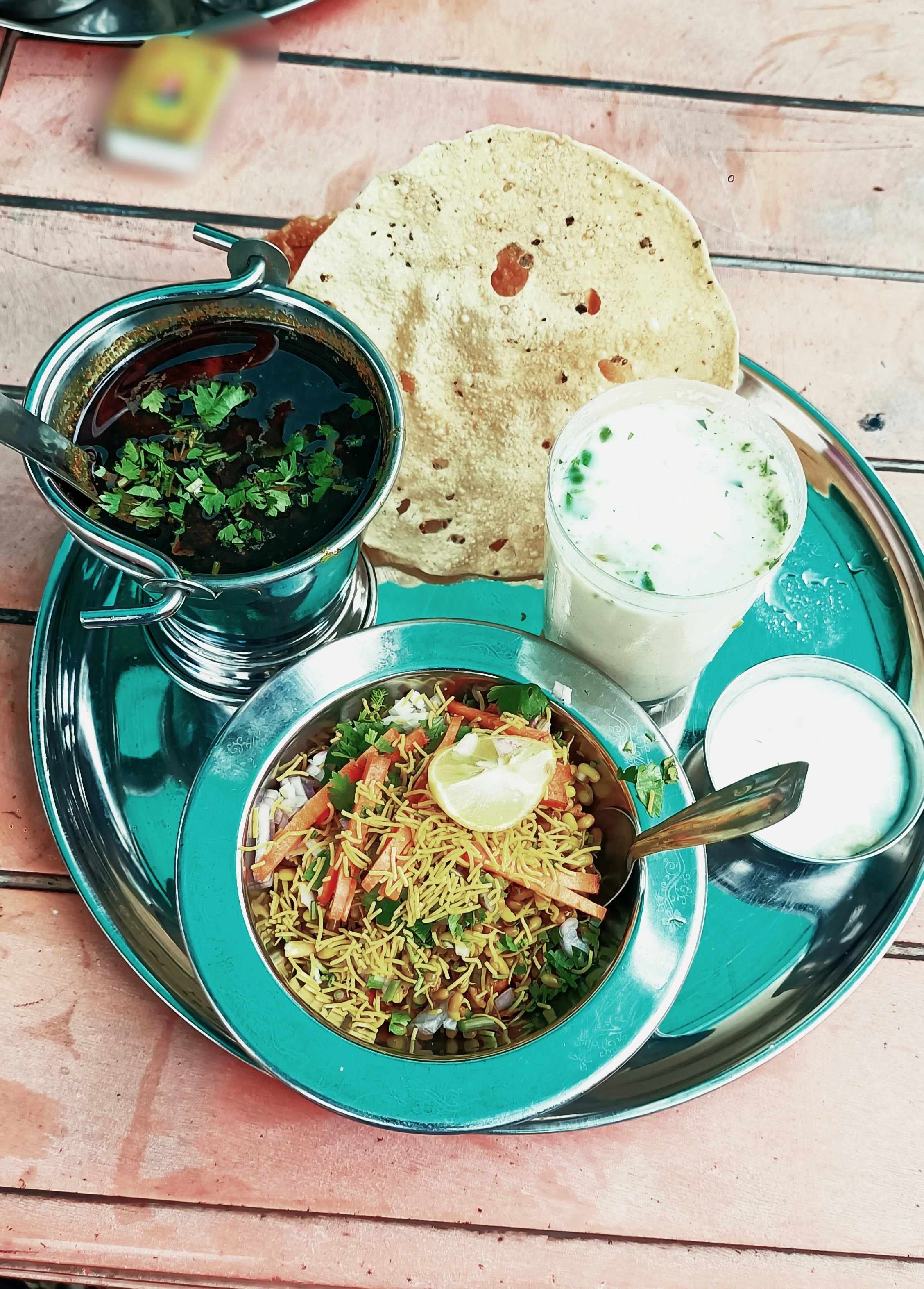 Vibrant street cafe bowl: noodles, condiments, and frothy lassi on a teal tray