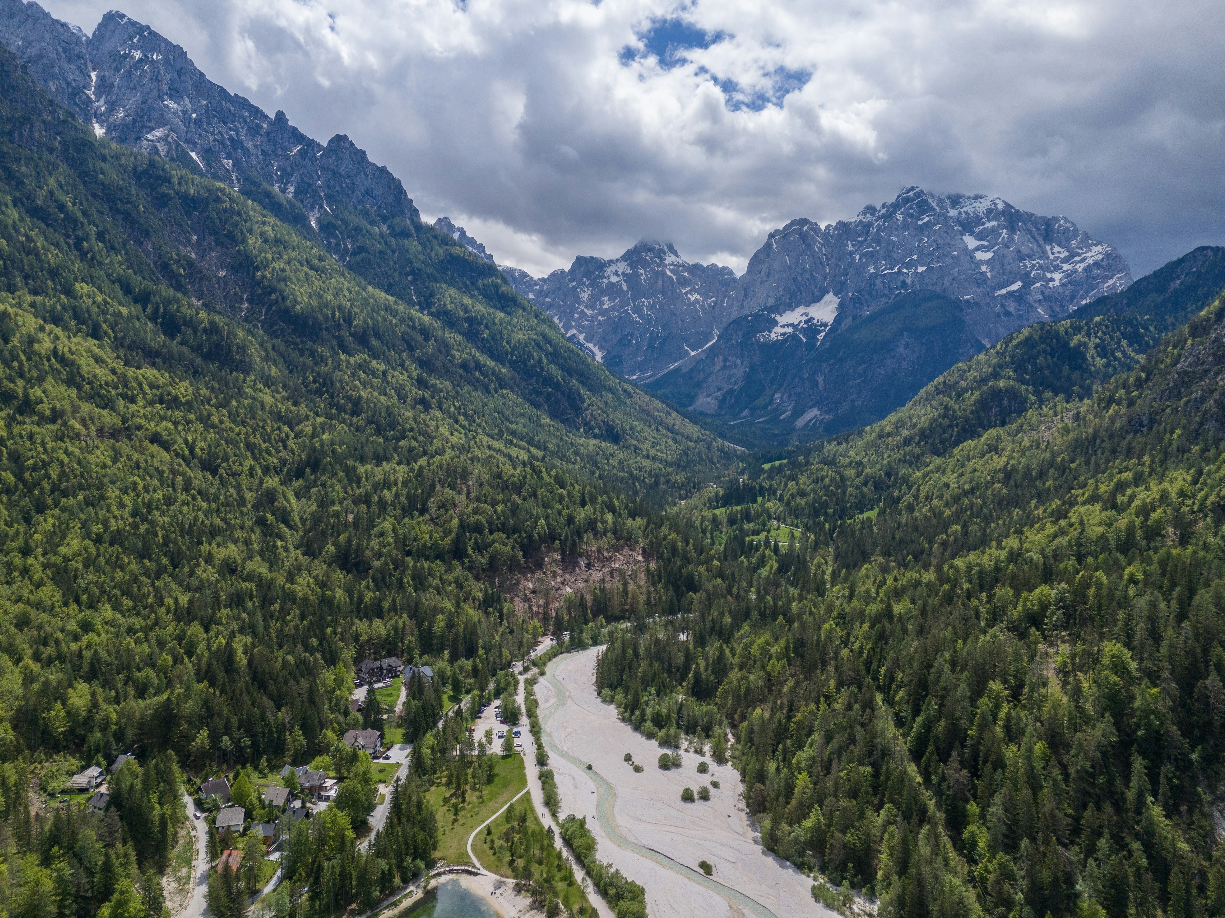 Aerial view of a lush green valley surrounded by towering mountains under a partly cloudy sky.