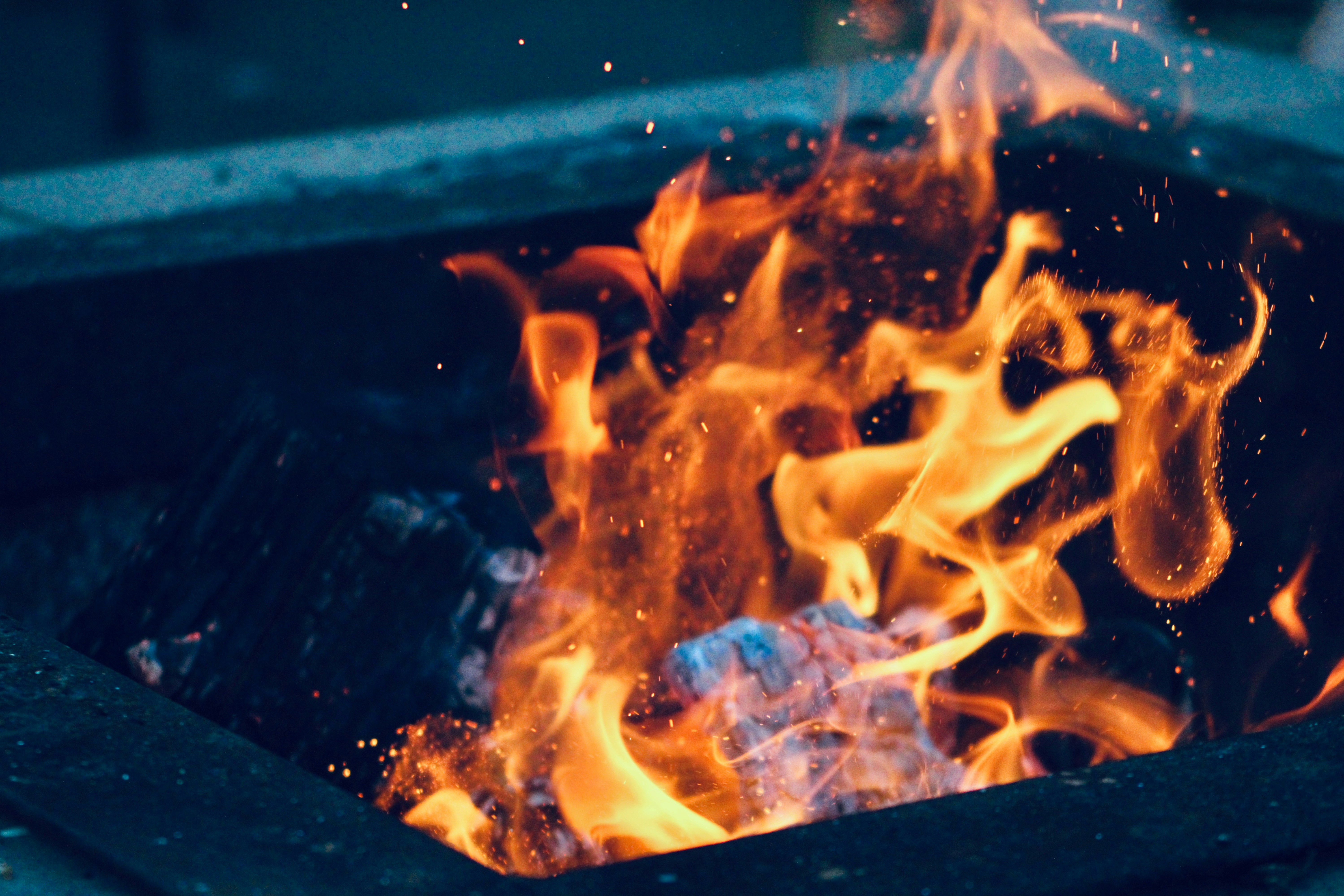 Vibrant flames flicker and swirl around glowing embers in a fire pit, creating a mesmerizing display of light and movement.