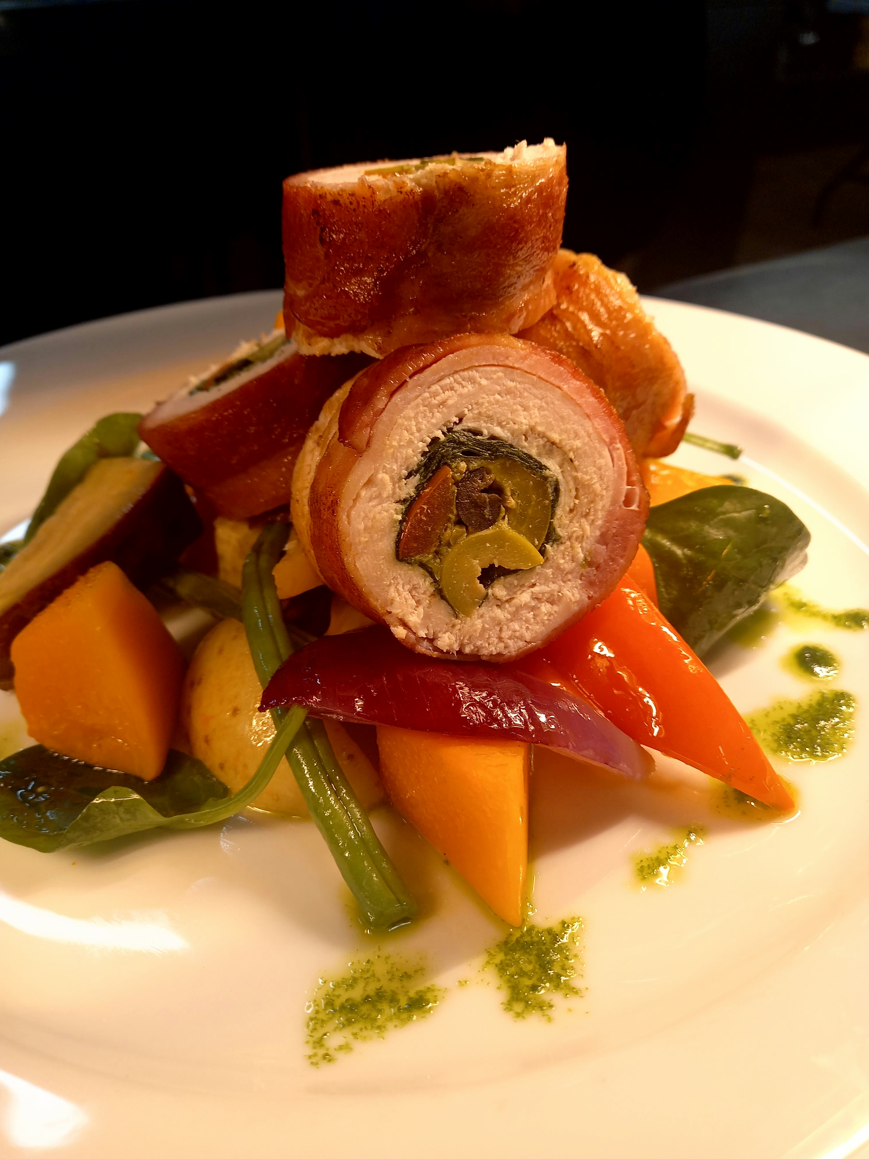 Sauteed vegetables and a stacked roulade centerpiece on a white plate with herbs embellishing the sauce.