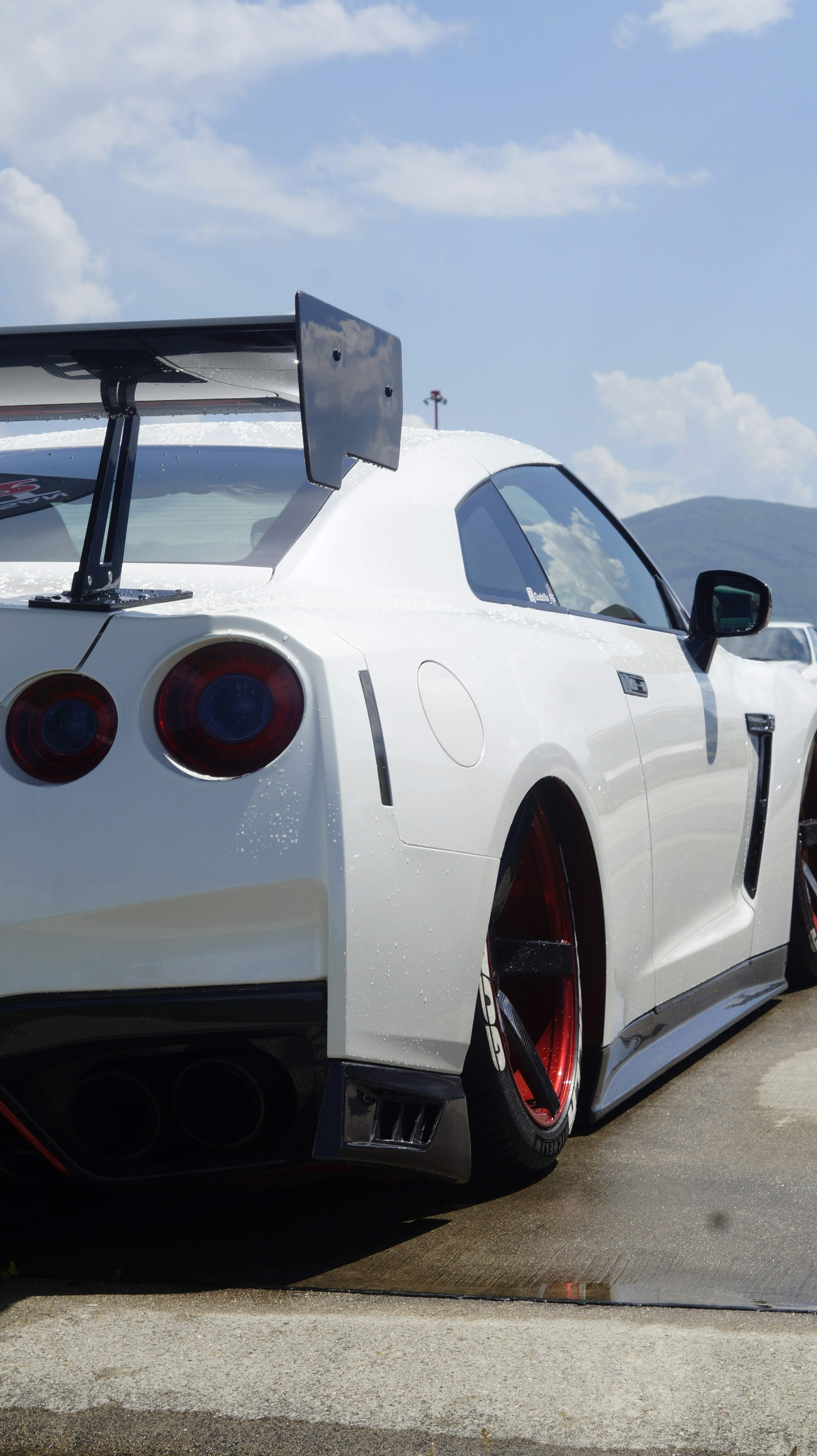 Modified white sports car with a prominent rear wing and red accents, showcasing sleek lines and performance features.