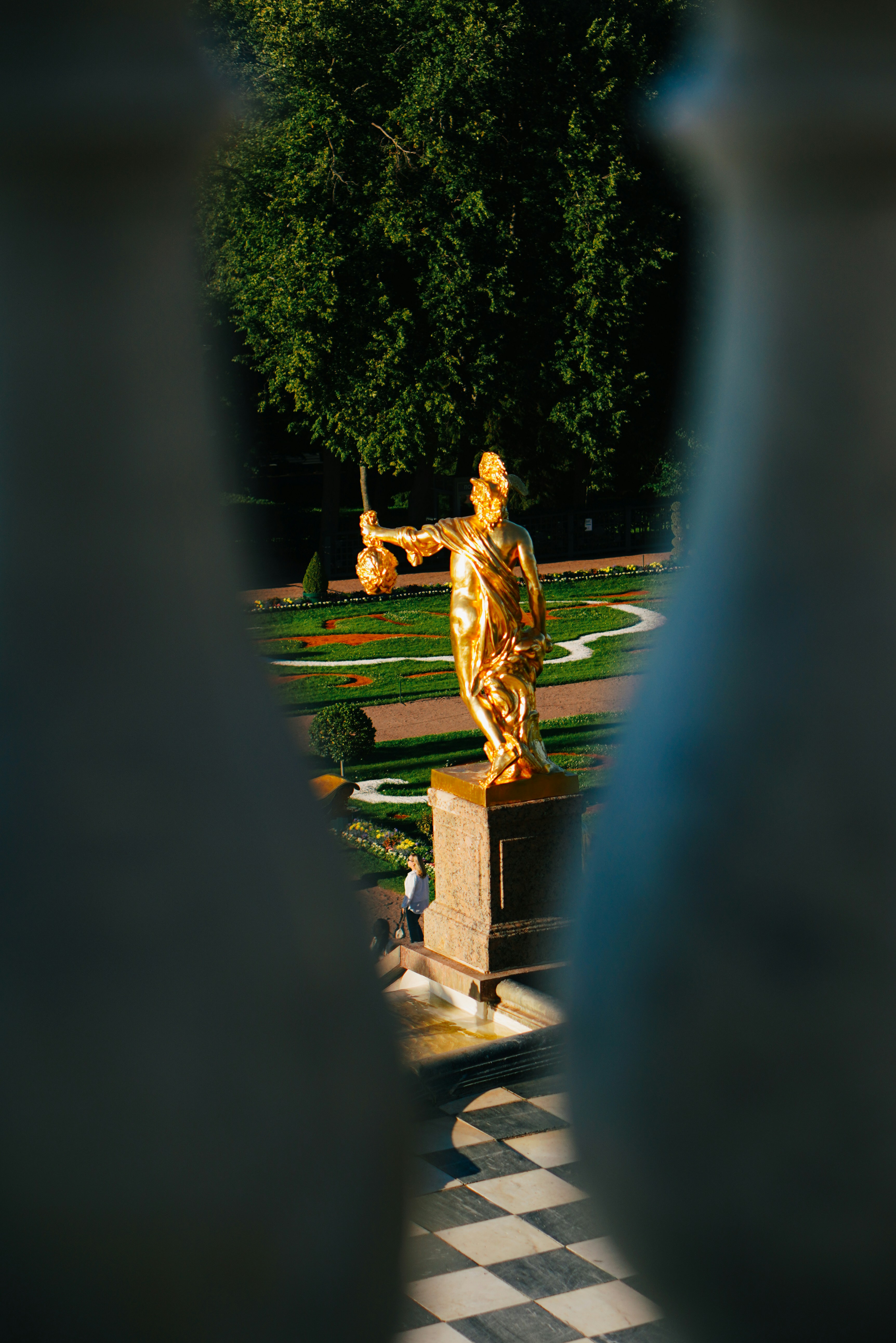 Through a Narrow Aperture: A Gilded Statue in a Formal Garden