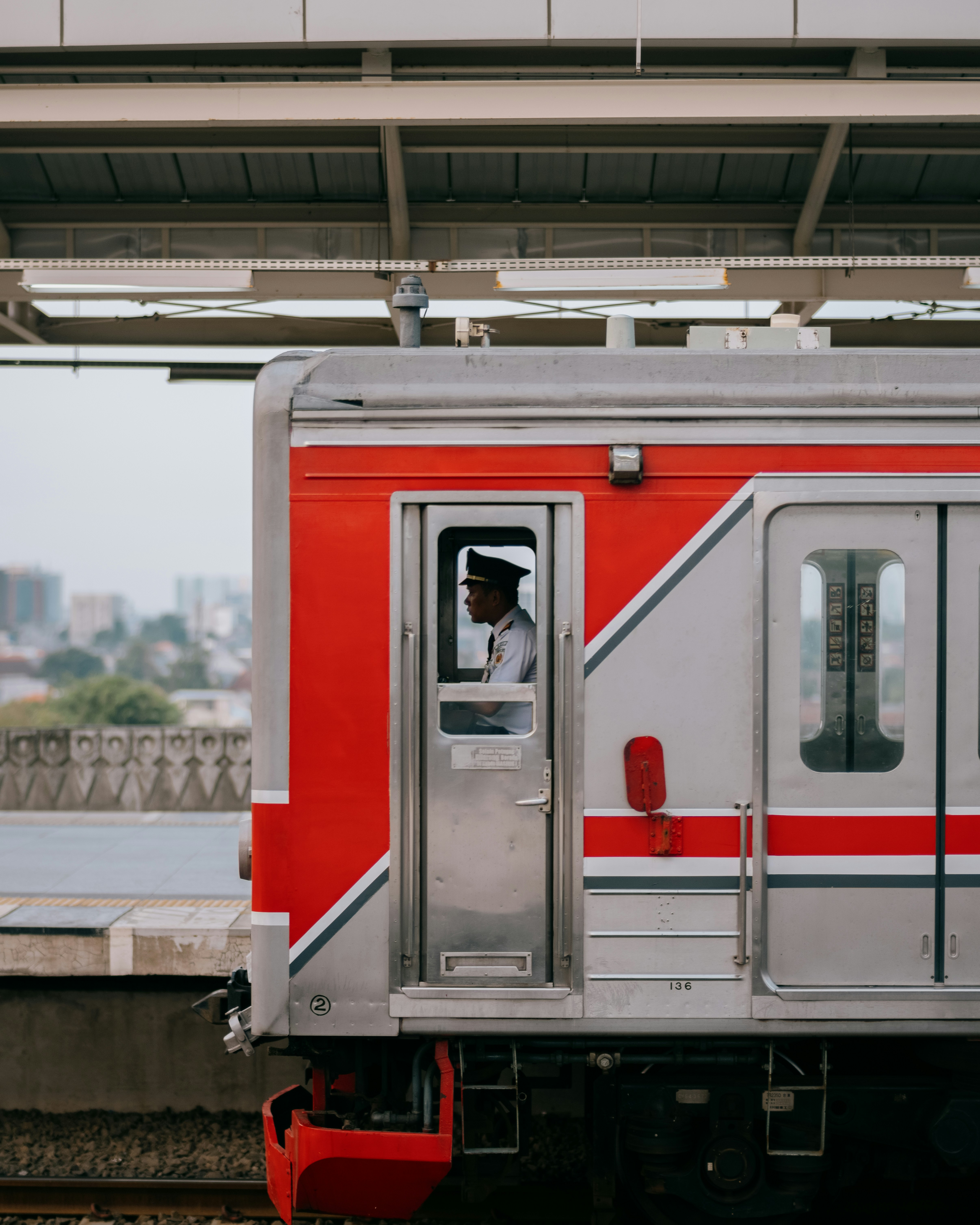 Conductor peering out from the driver's cabin of a vibrant red train at a bustling station.