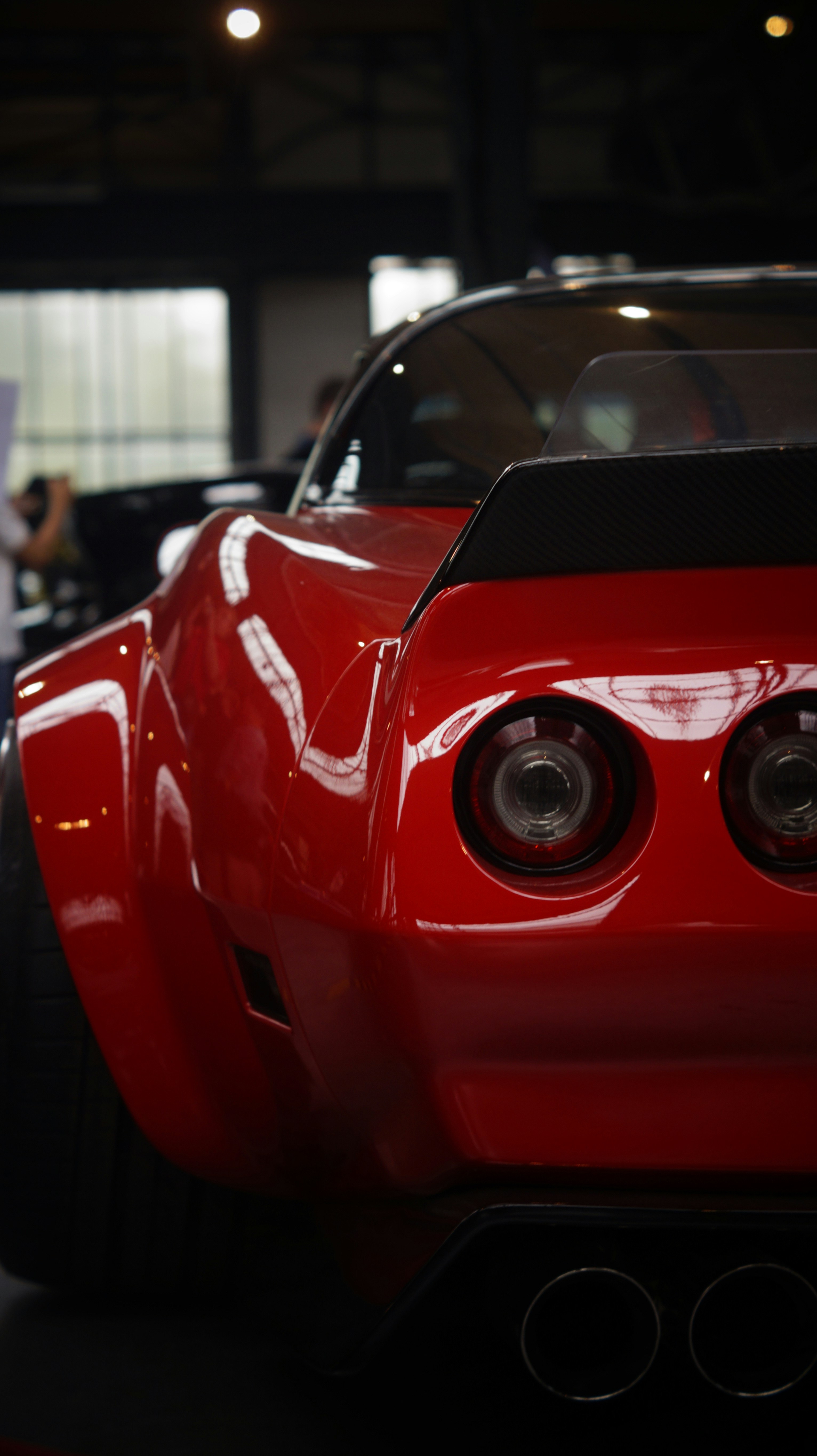 Sleek red sports car with dual exhausts and aerodynamic design in a dimly lit garage.
