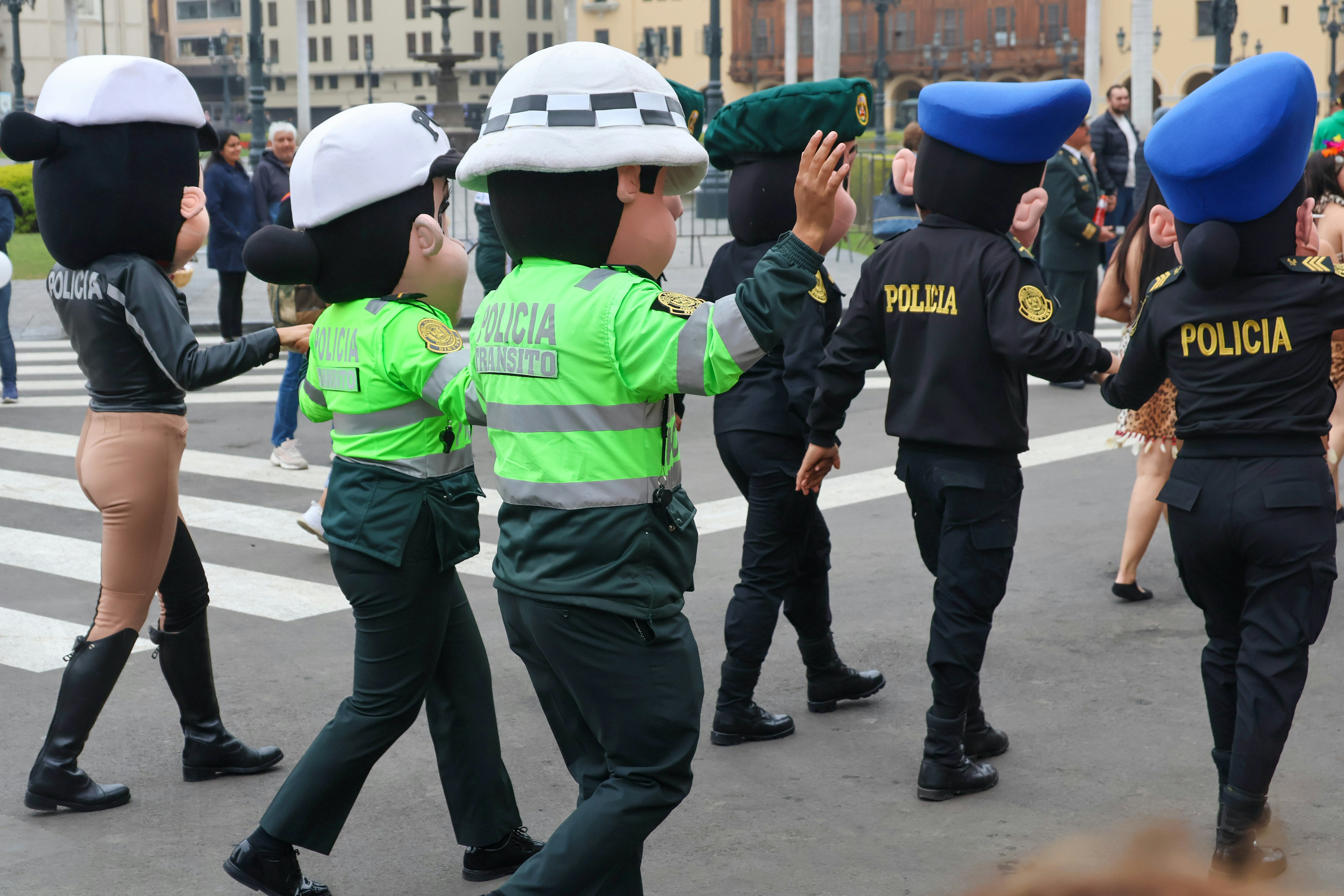 Parade scene featuring uniformed officers wearing bright green vests and white helmets marching down a city street. A crowd watches them pass in the background.