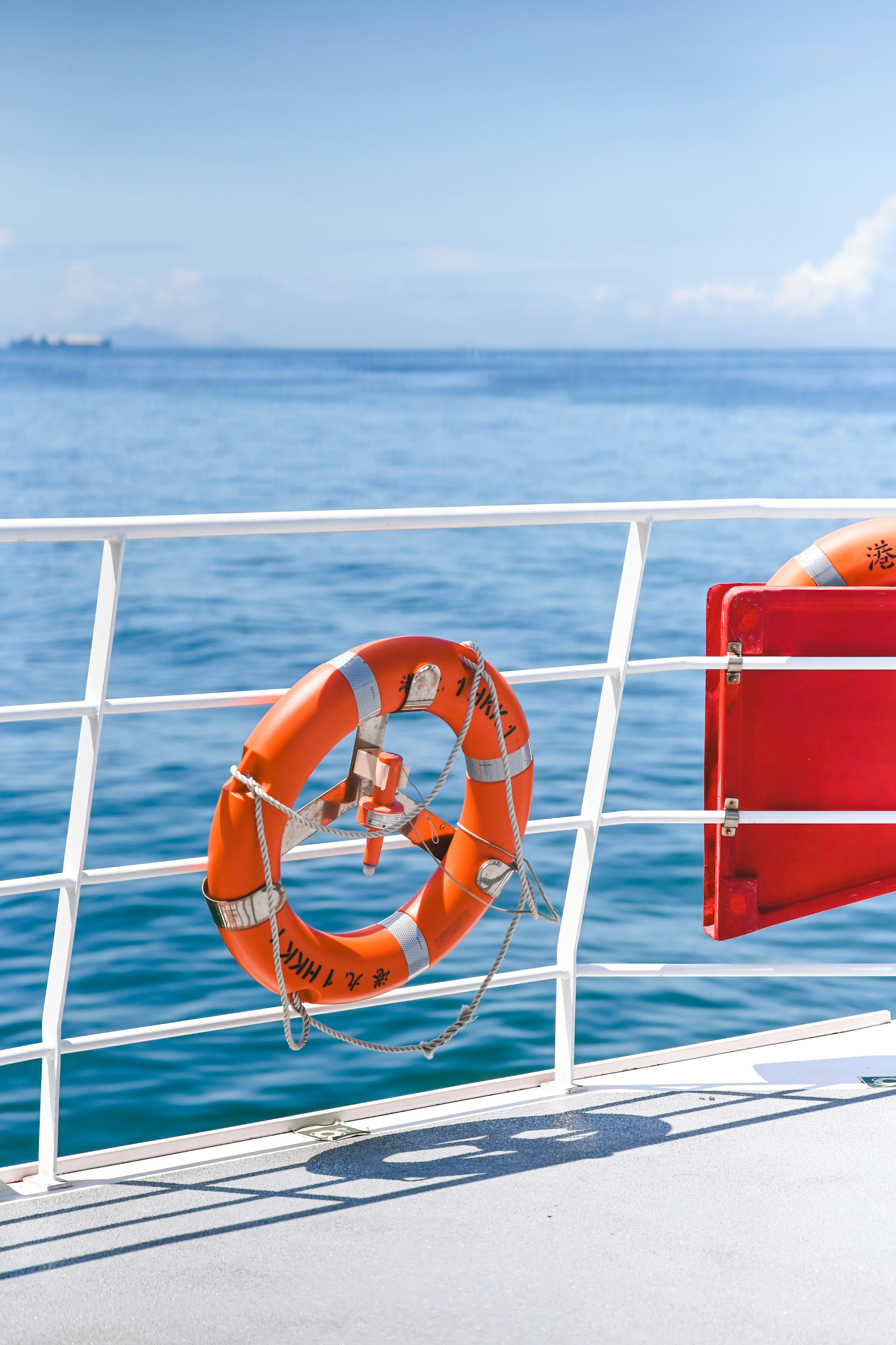 Bright orange lifebuoy secured to a boat railing, overlooking calm blue waters under a clear sky.