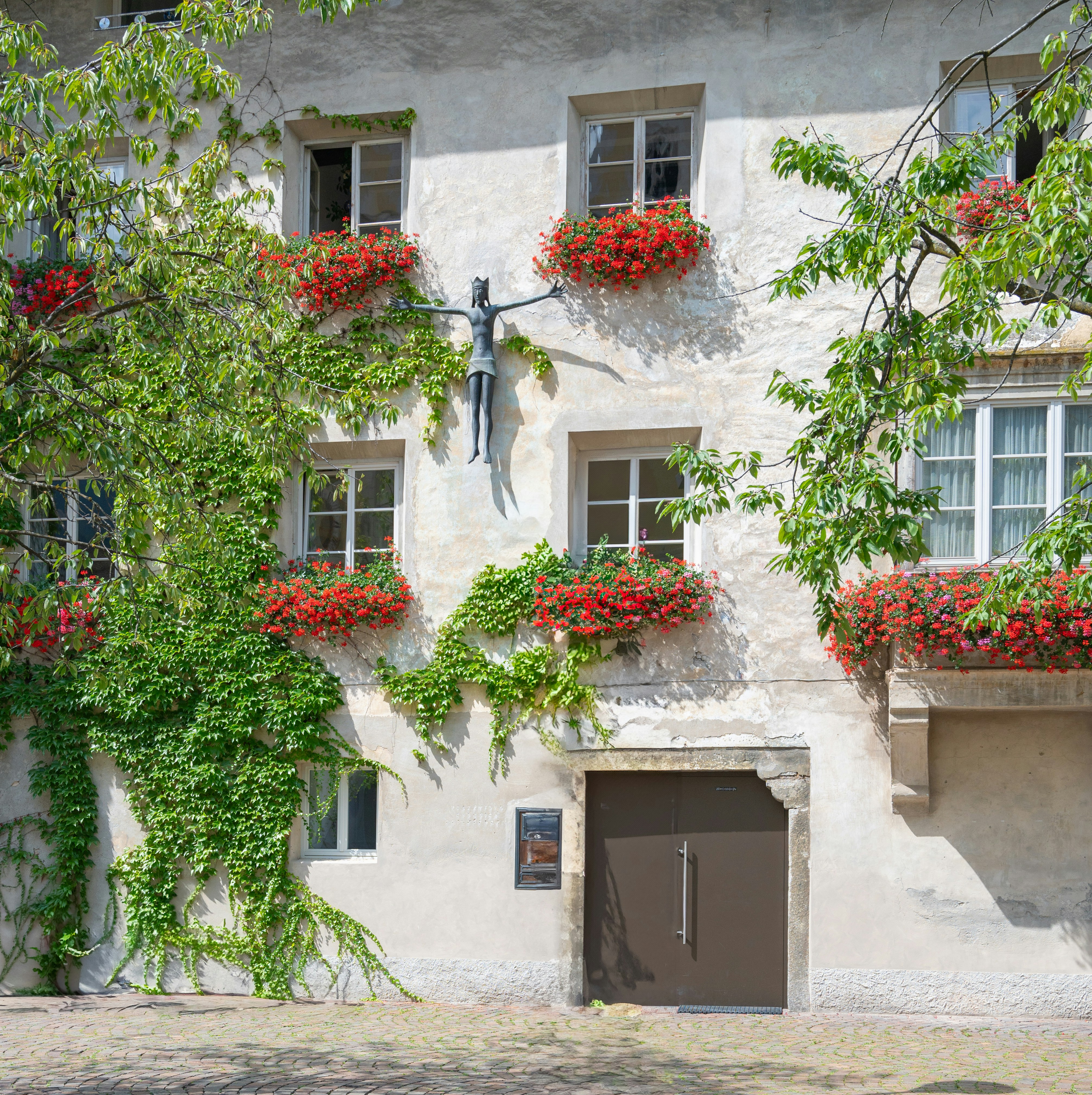 Crucifix Framed by Ivy and Crimson Window Boxes on a Sunlit Facade