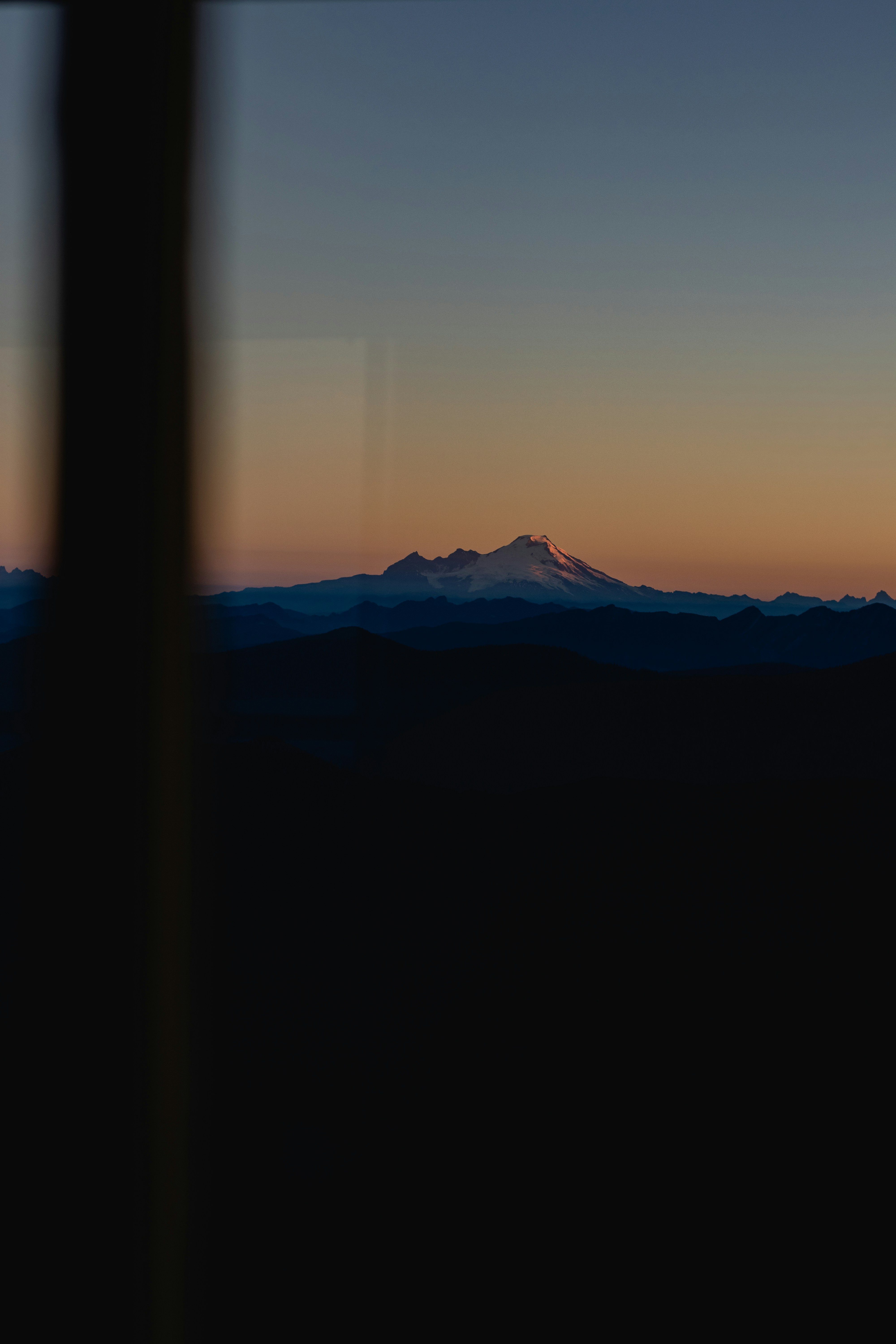 Twilight Summit Framed by Window: Snow-Capped Peak at Dusk