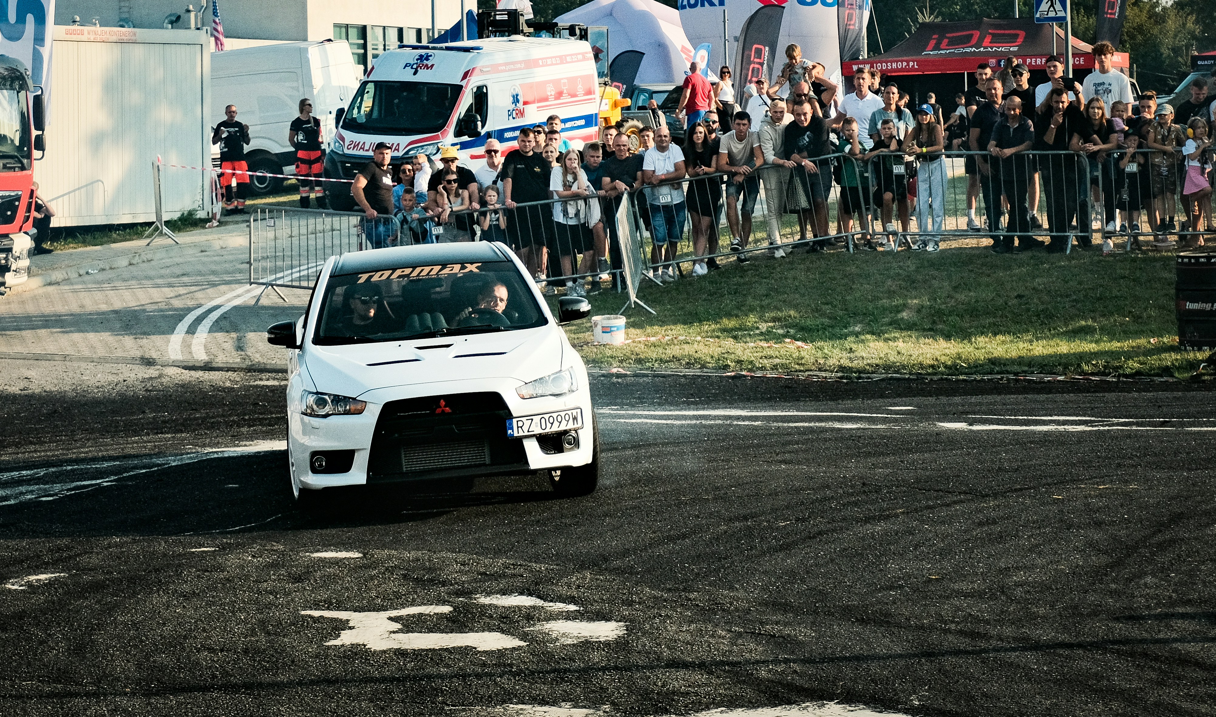 A white car driving down a street next to a crowd of people photo ...