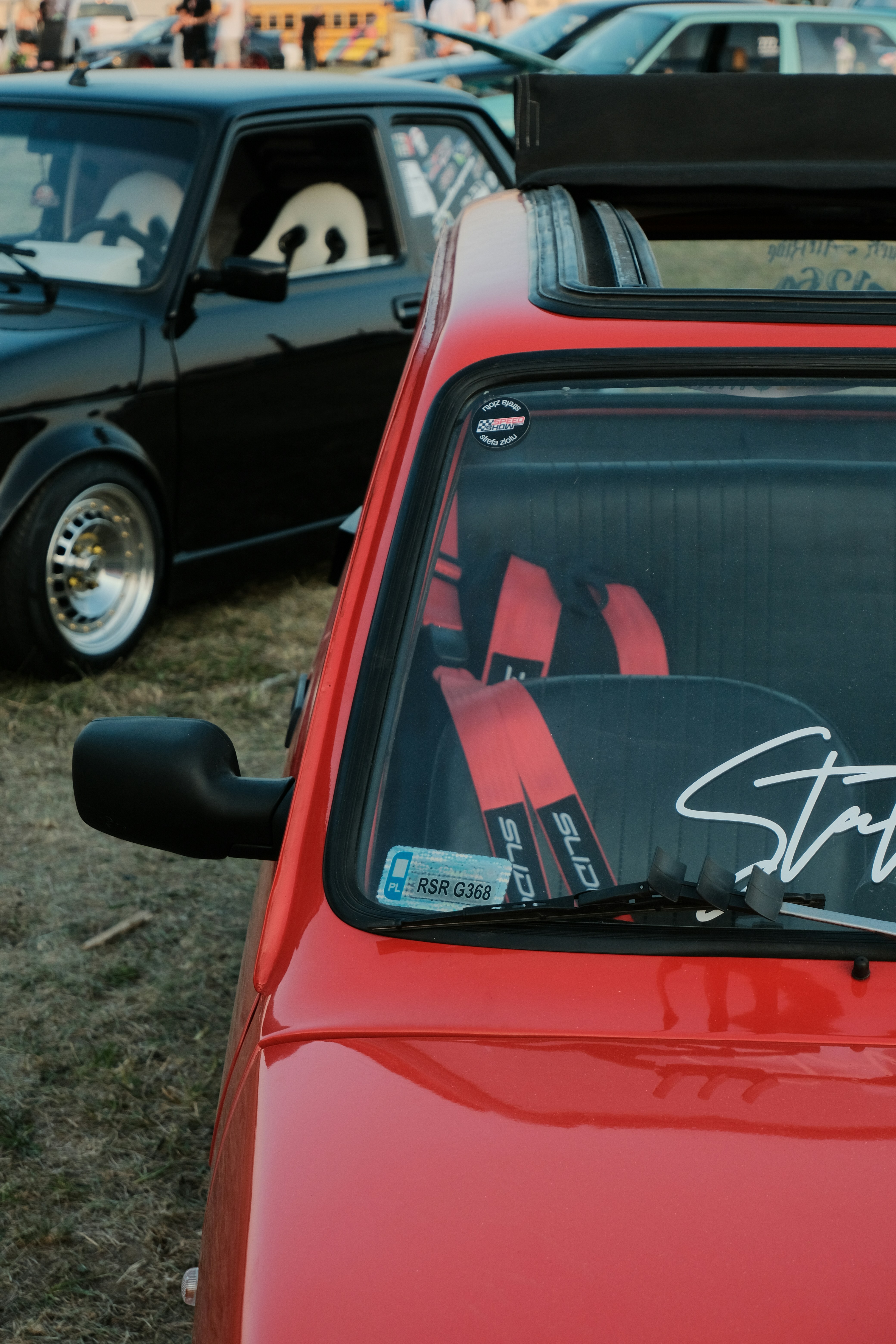 Crimson Coupe at the Car Meet: Racing Harnesses and a Silent Crowd of Classics