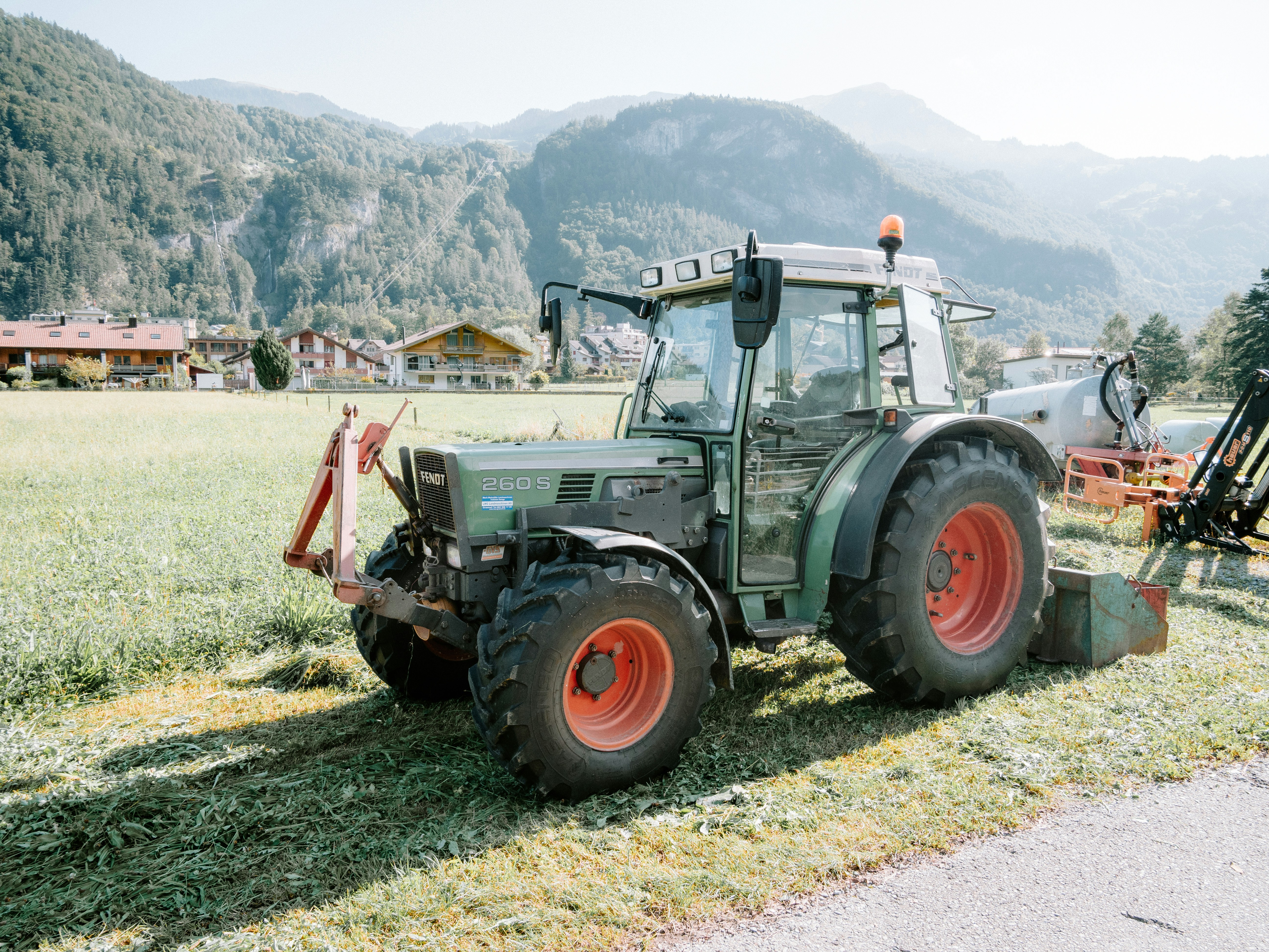 Alpine Tranquility: Green tractor with orange wheels in a sunlit meadow
