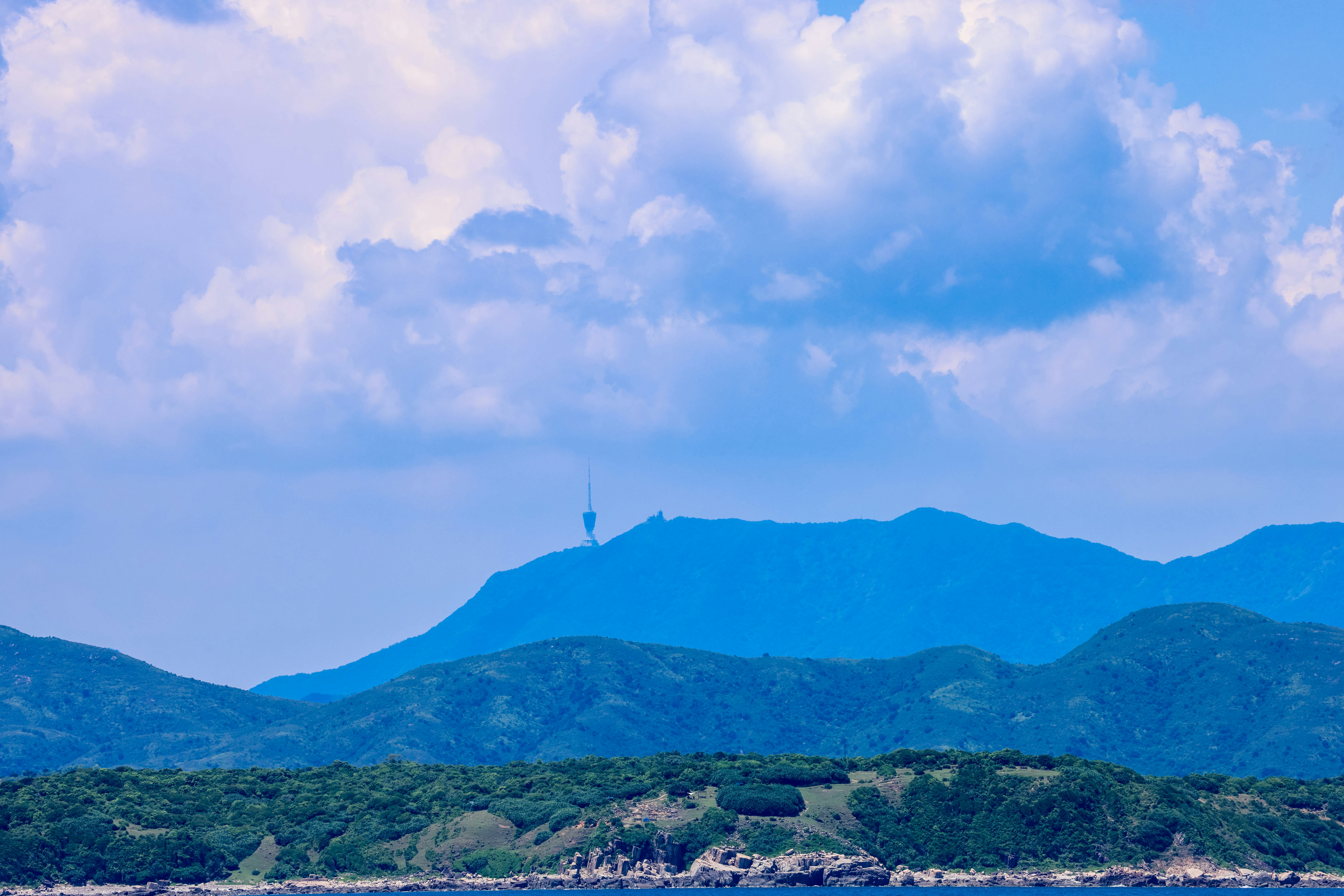Crest Beacon: A Lone Tower Crowns the Coastal Ridge Beneath a Drifting Blue Sky