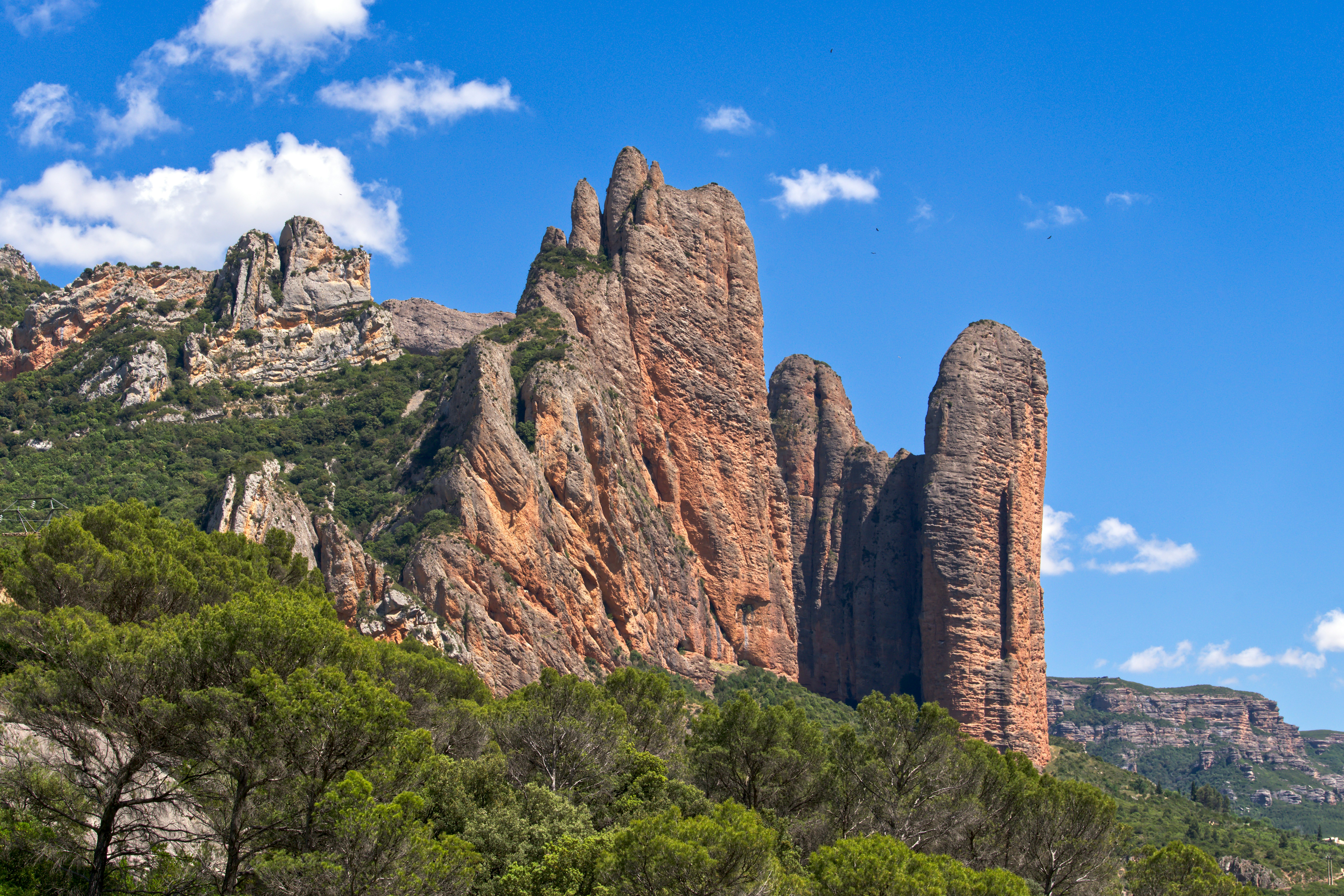 Towering rock formations rise above lush greenery under a clear blue sky.
