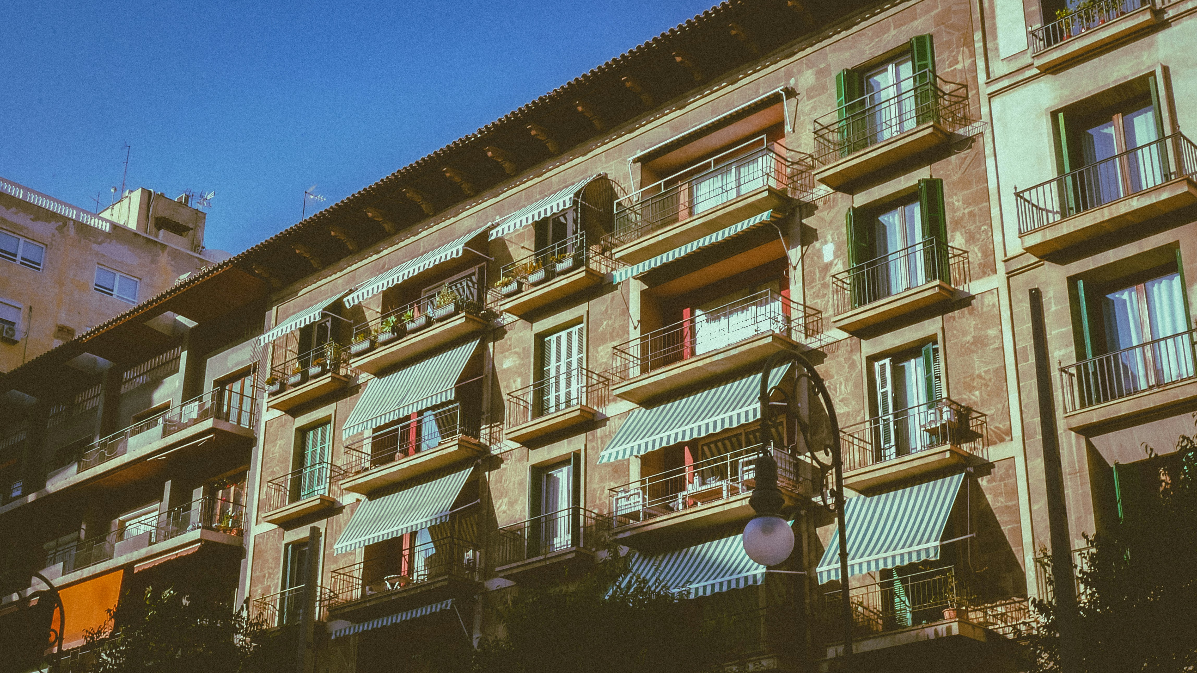 Sunlit building facade with numerous windows and balconies against a clear blue sky.