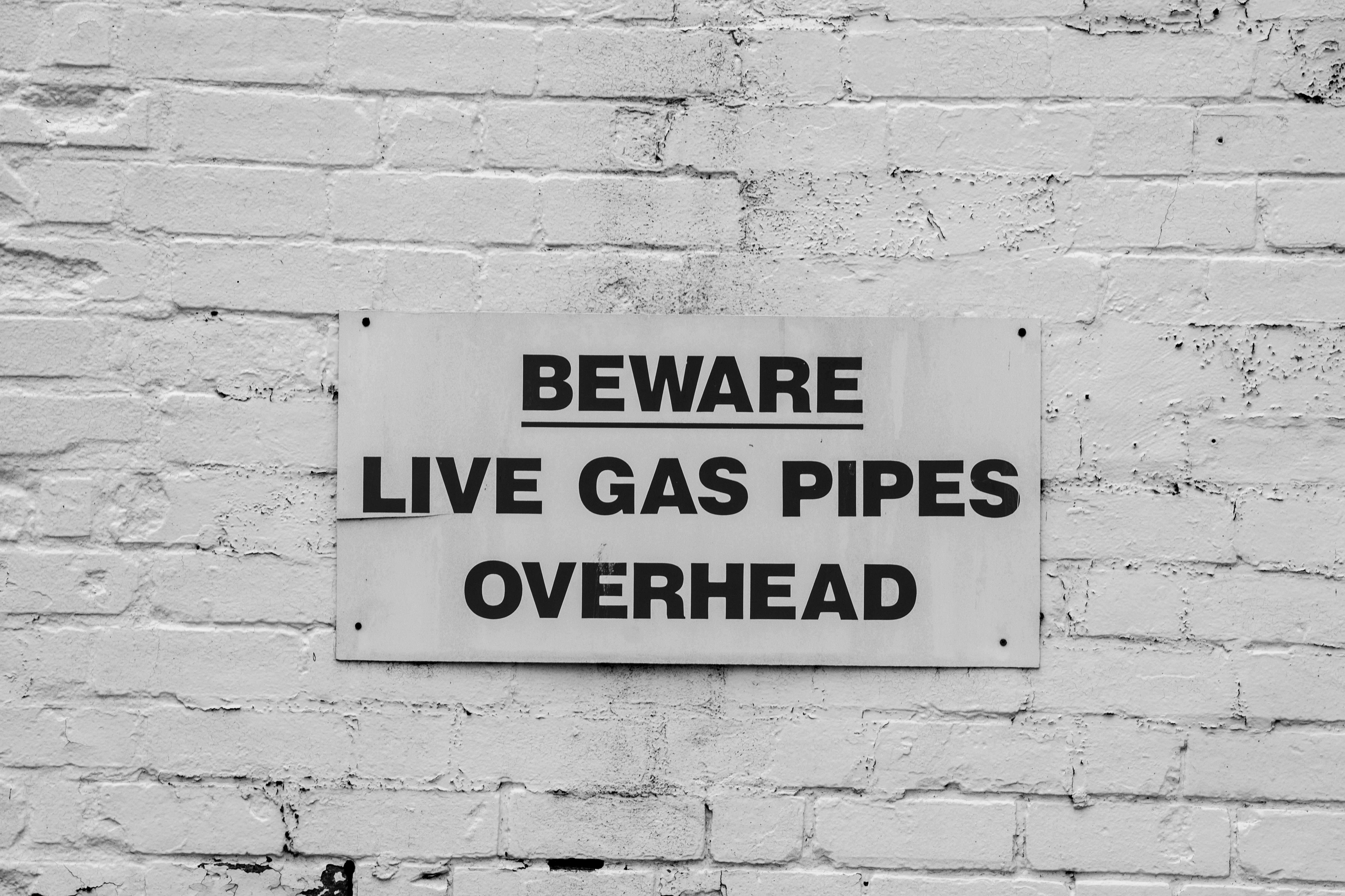A brick wall with a sign on it stating beware live gas pipes overhead ...
