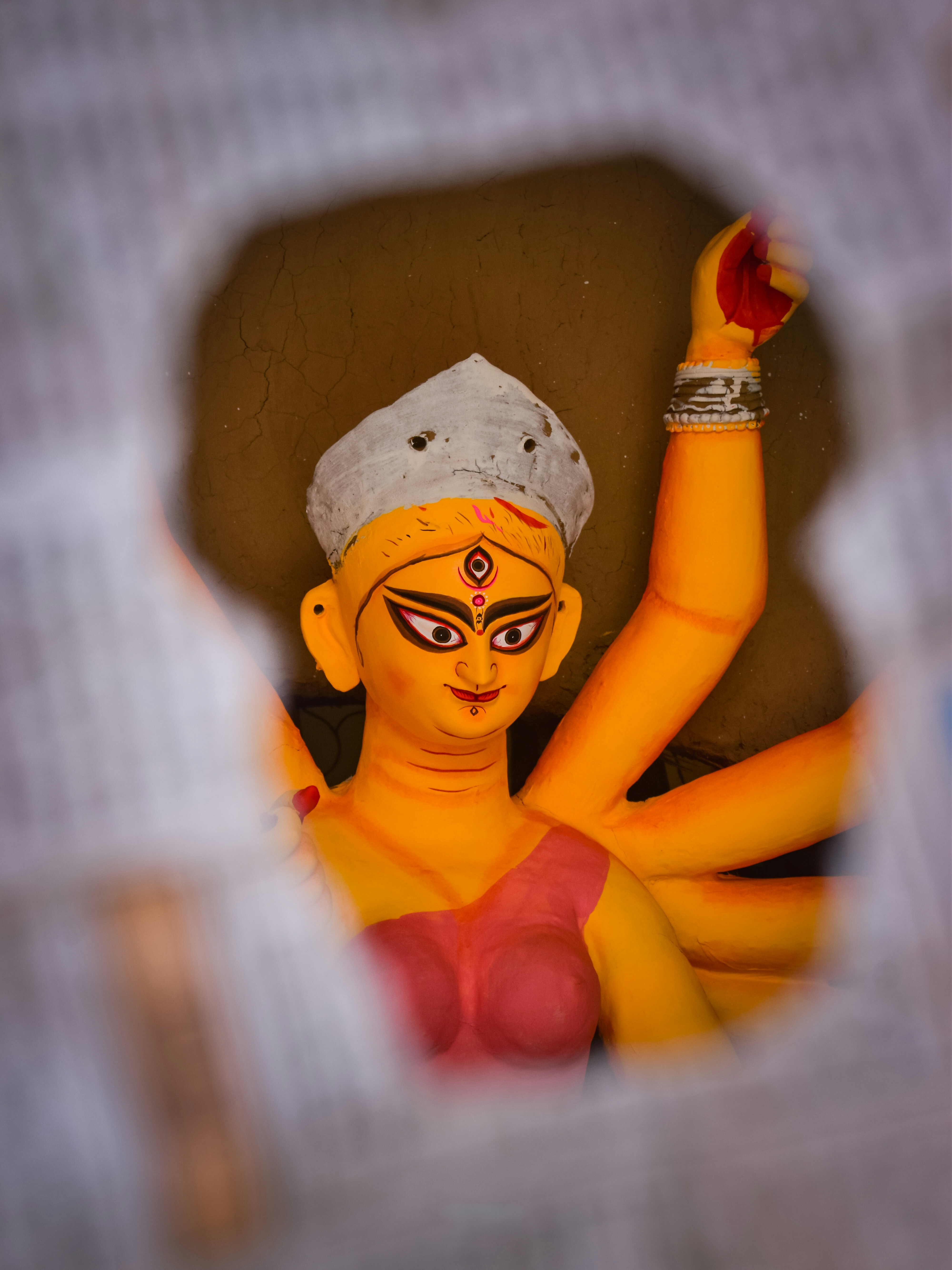 Framed Flame: A Hindu Goddess Statue Peering Through a Frayed Window