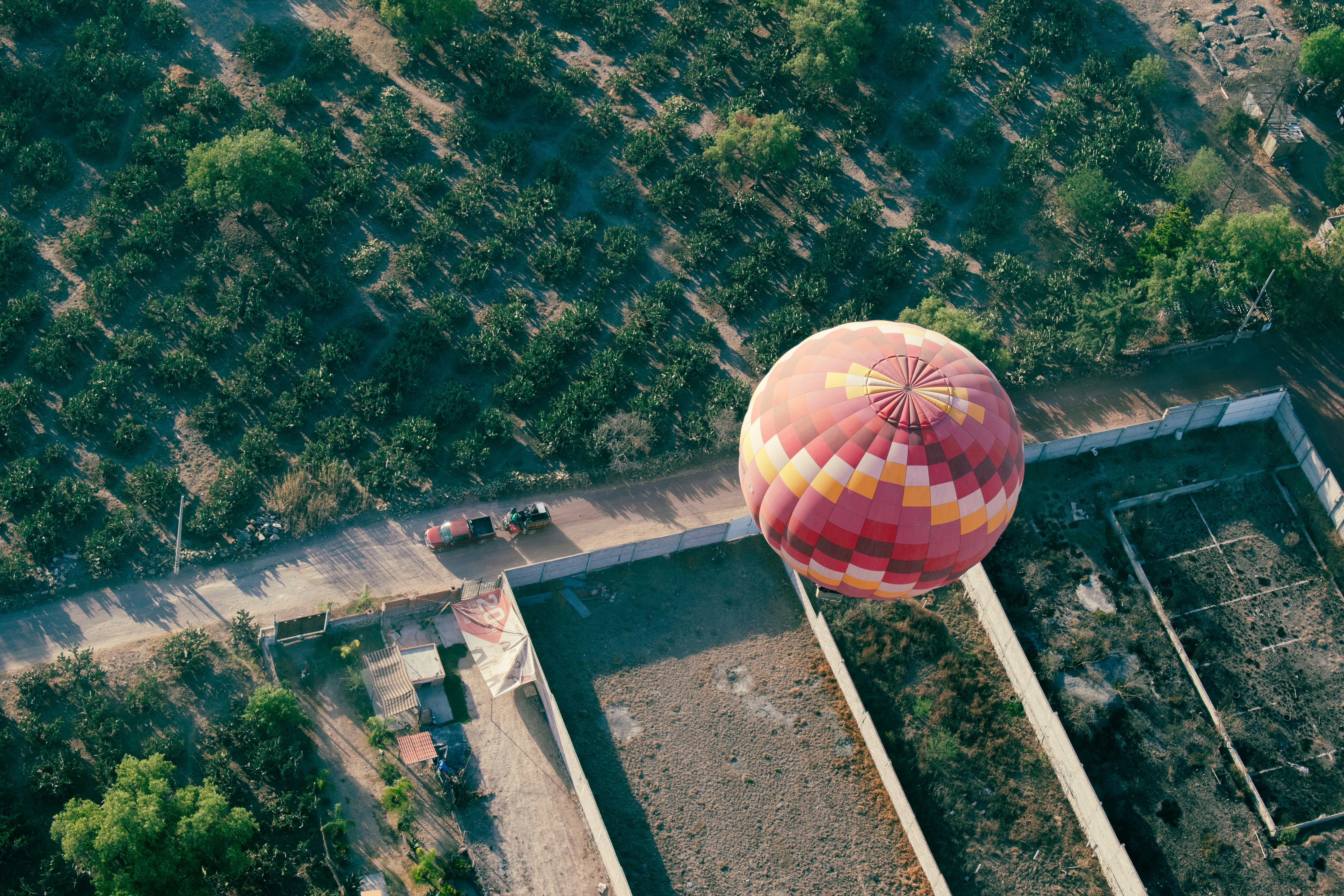 Hot air balloon floats above patterned fields and pathways, casting a soft shadow on the landscape.