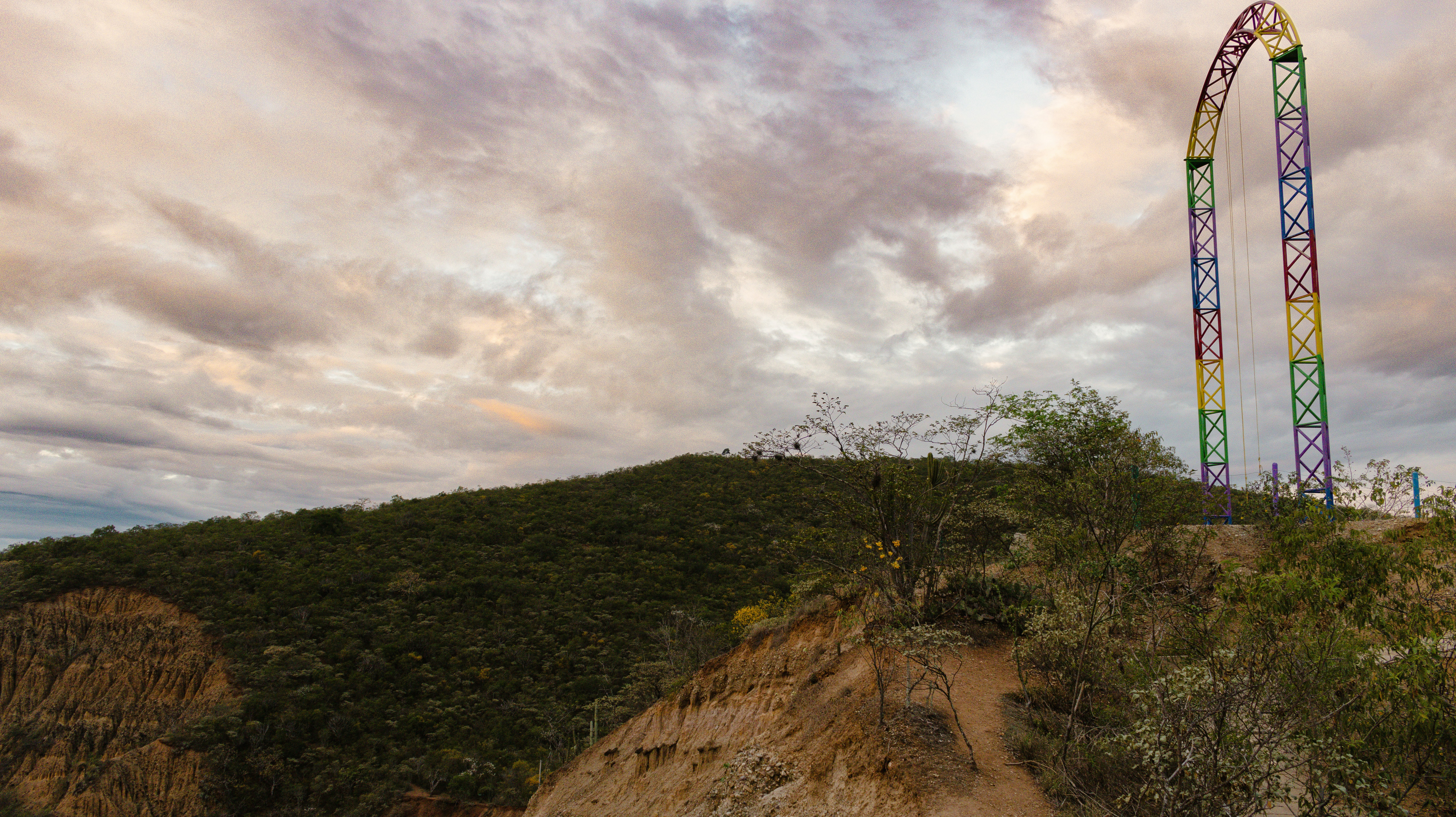Roller coaster ascending above a rugged hill under a dynamic evening sky.