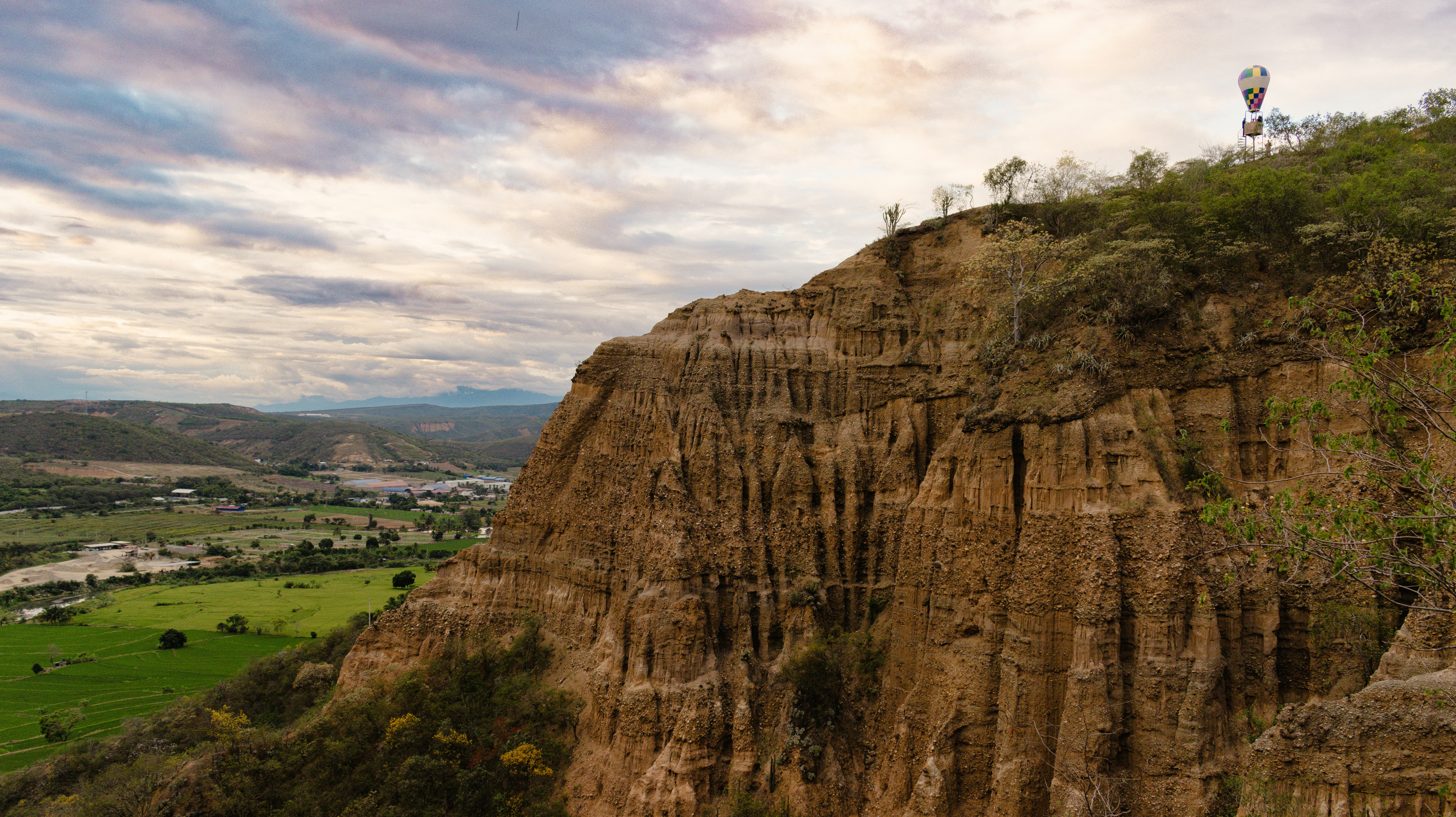 Hot air balloon floating above rugged, steep cliffs with a vast landscape in the background.