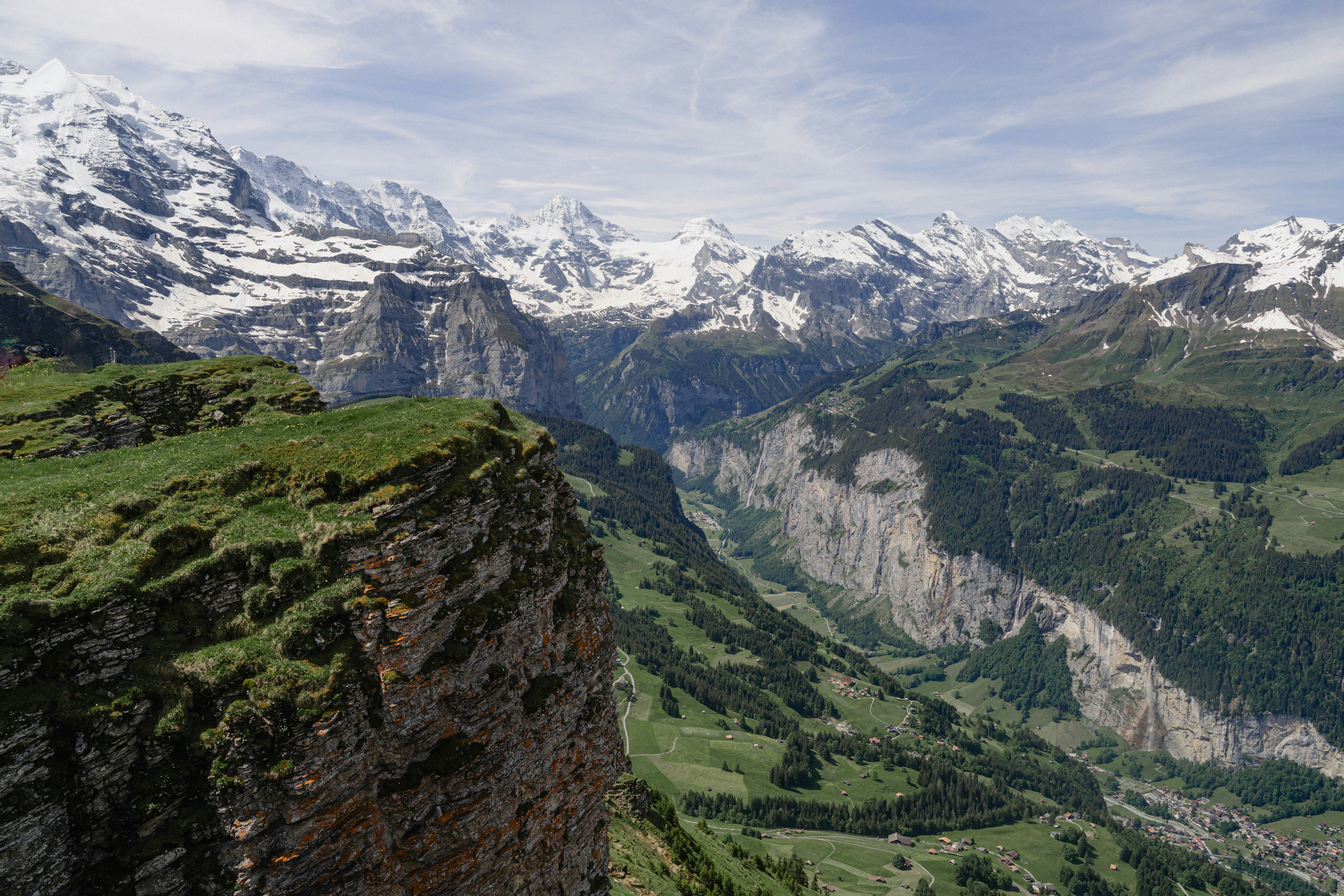 Vast mountain range with snow-capped peaks and lush green valleys under a bright blue sky.