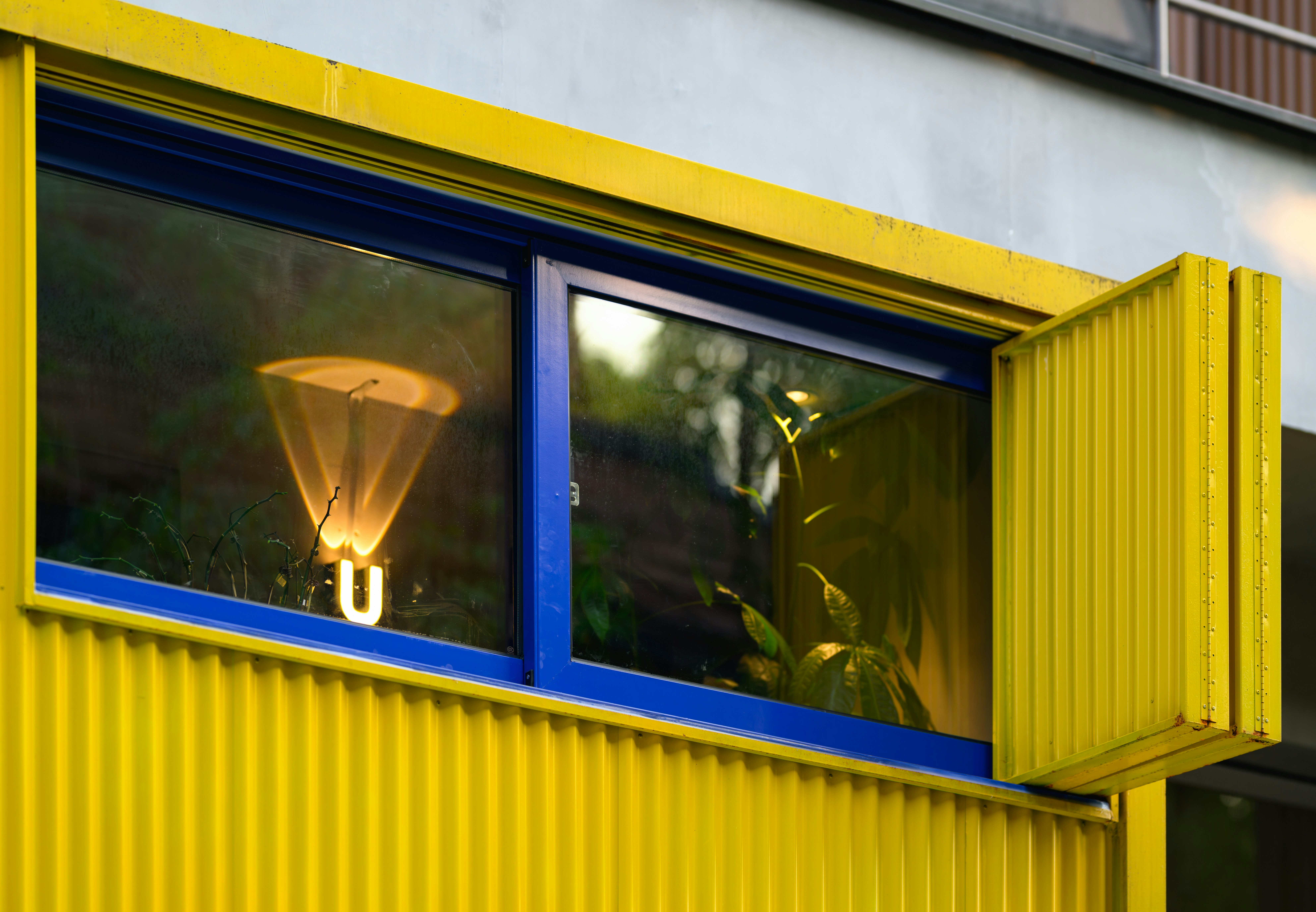 Sunlit yellow corrugation frames a cobalt window glowing with interior warmth