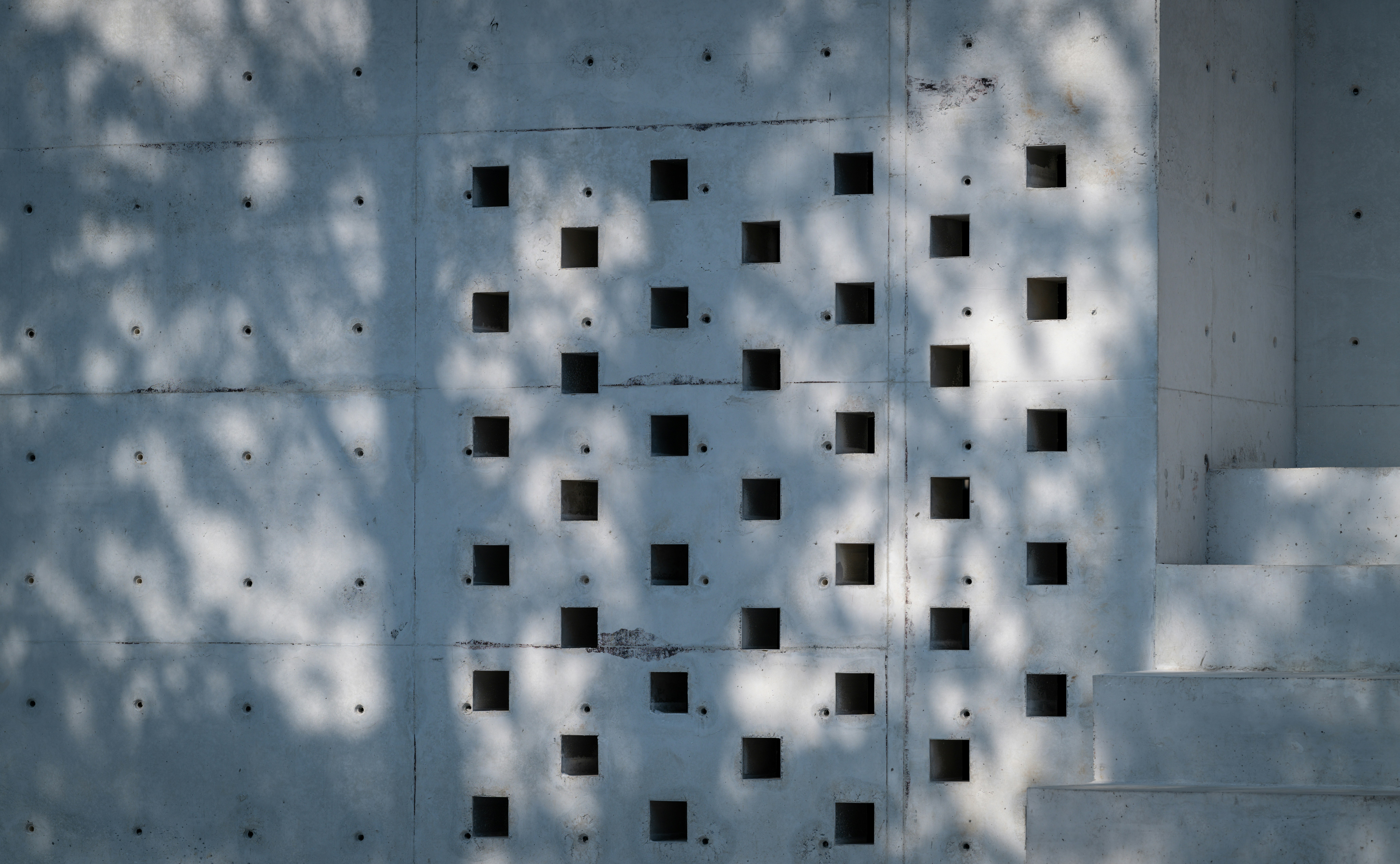 Textured concrete wall with a pattern of square cutouts, casting intriguing shadows that play across the surface.