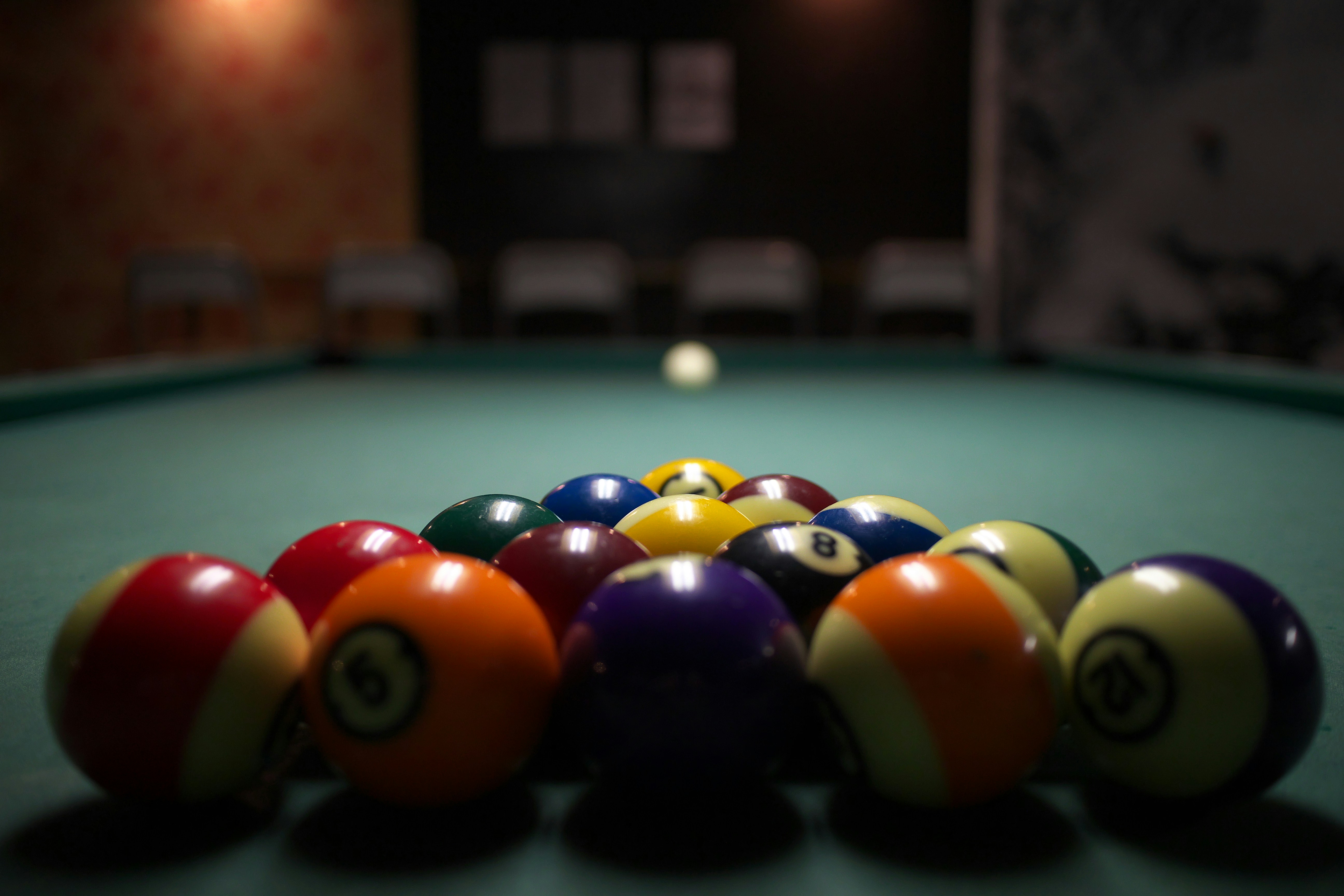 Photograph of a billiards table with colorful balls clustered in the foreground, sharp on the front balls and fading to a dark background.