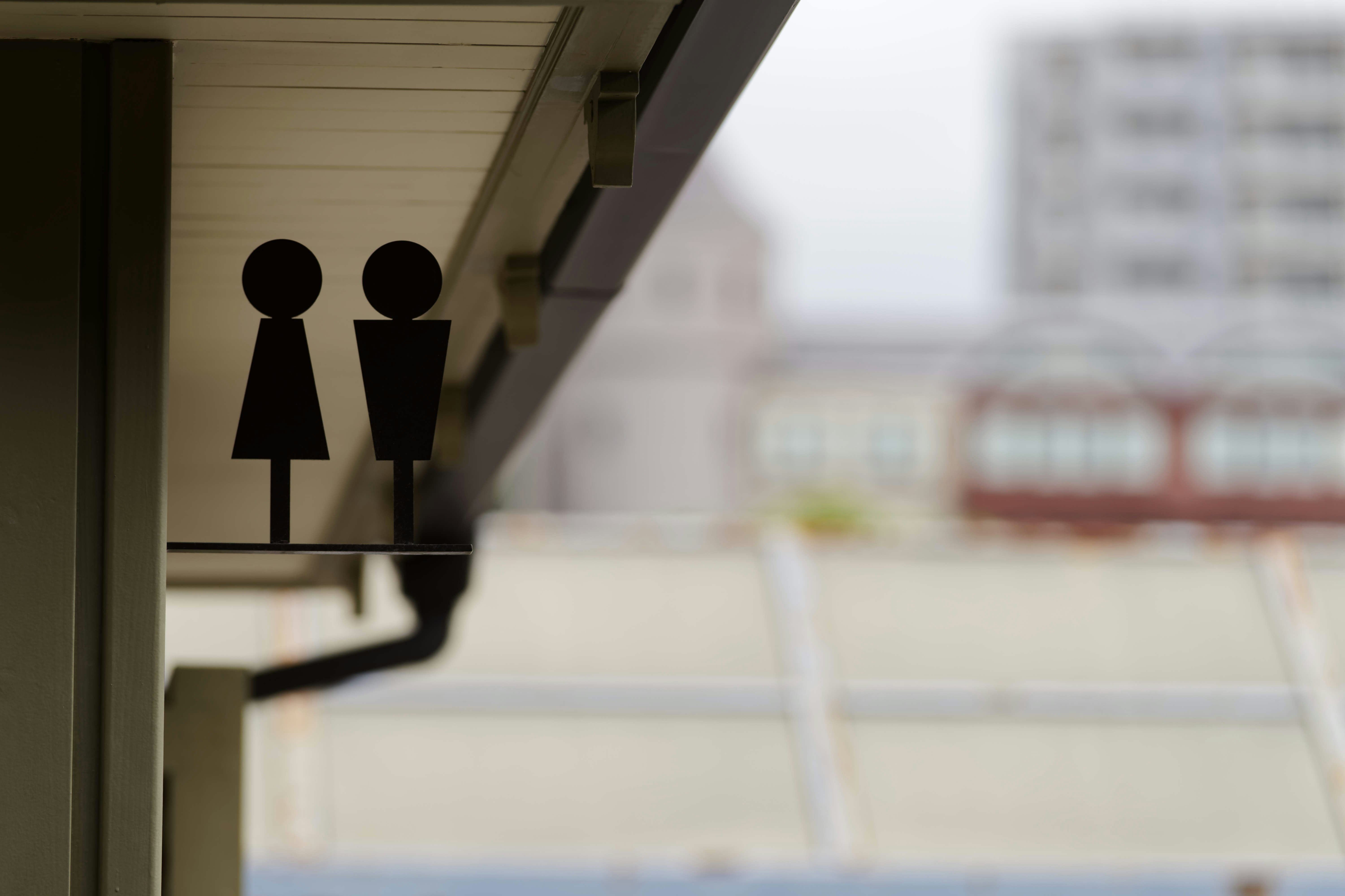 Two Silhouettes Under an Eave: A Restroom Sign in a Quiet City Blur