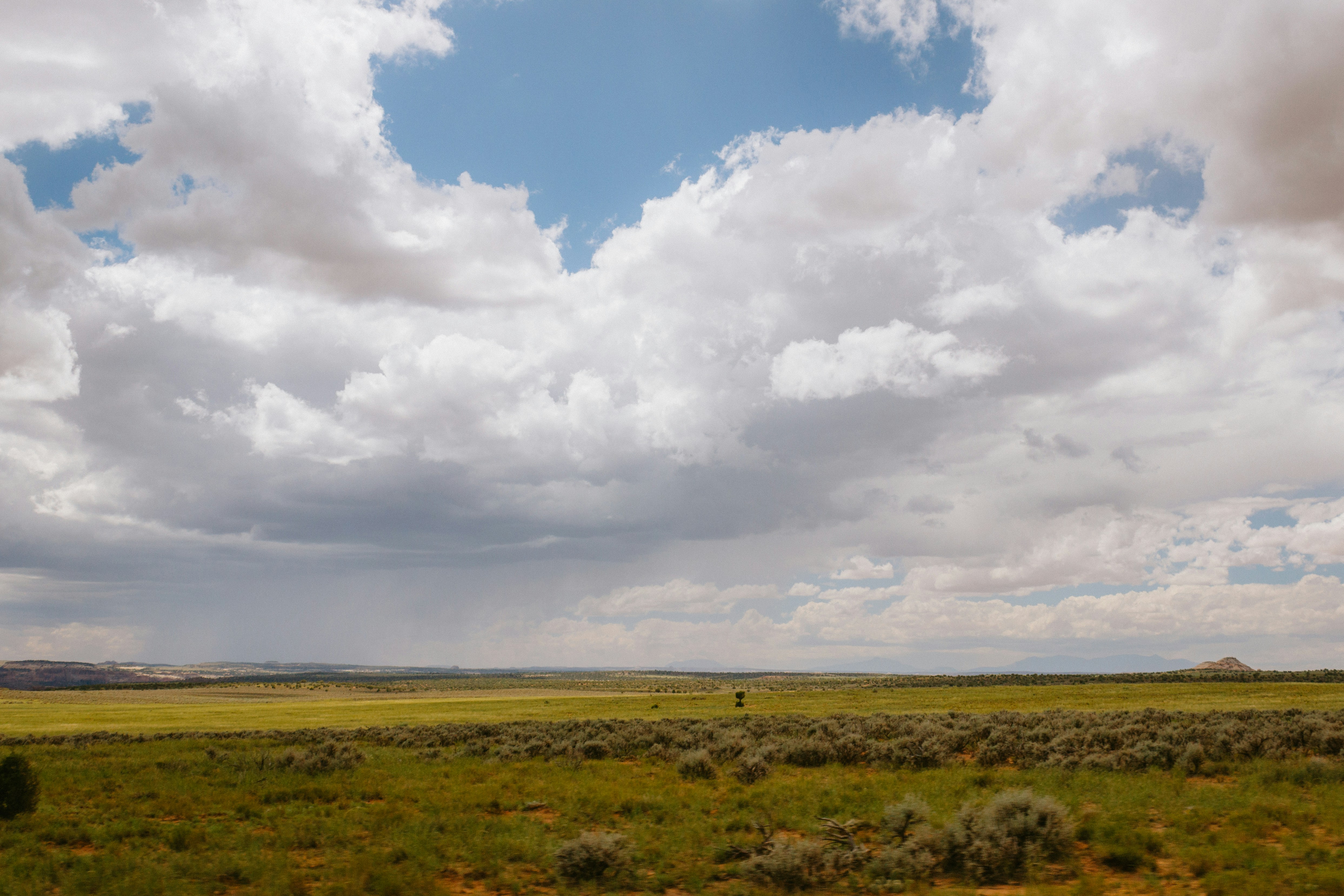 Expansive landscape showcasing a blend of grassy plains and dramatic cloud formations under a bright sky.