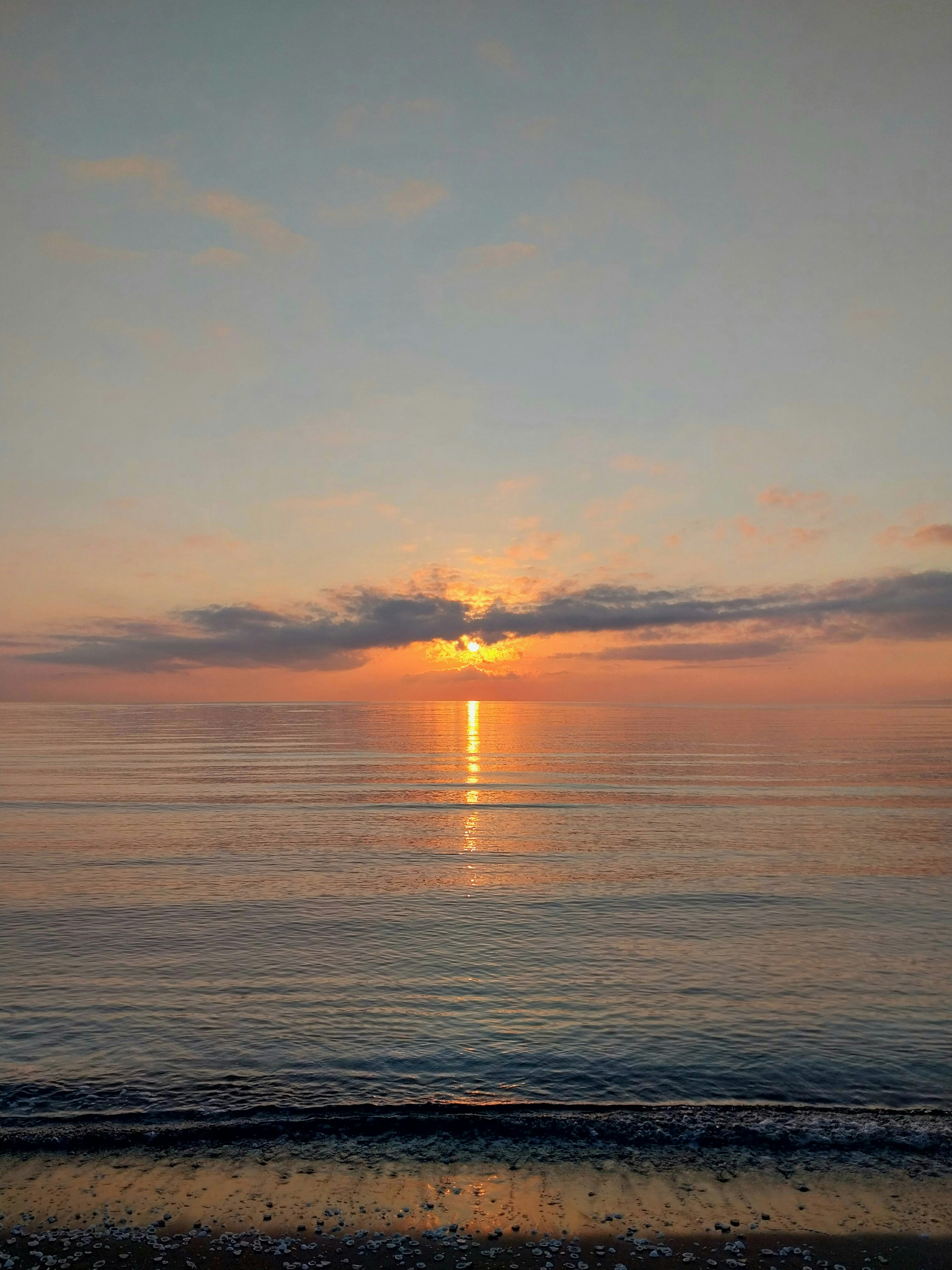 The sun is setting over the water on the beach photo – Free Sunrise ...